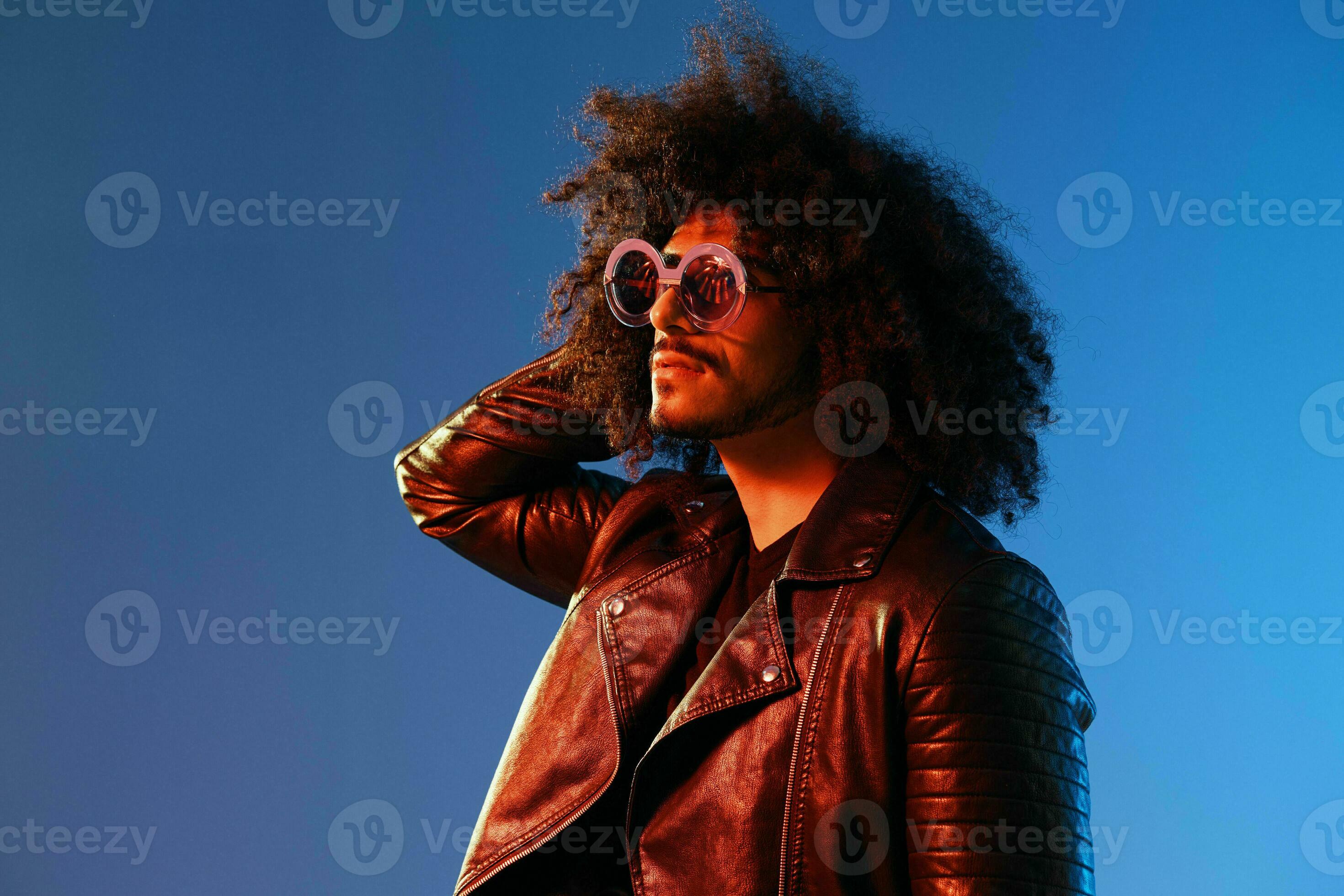 Portrait of a stylish man with curly hair with glasses smile on blue ...