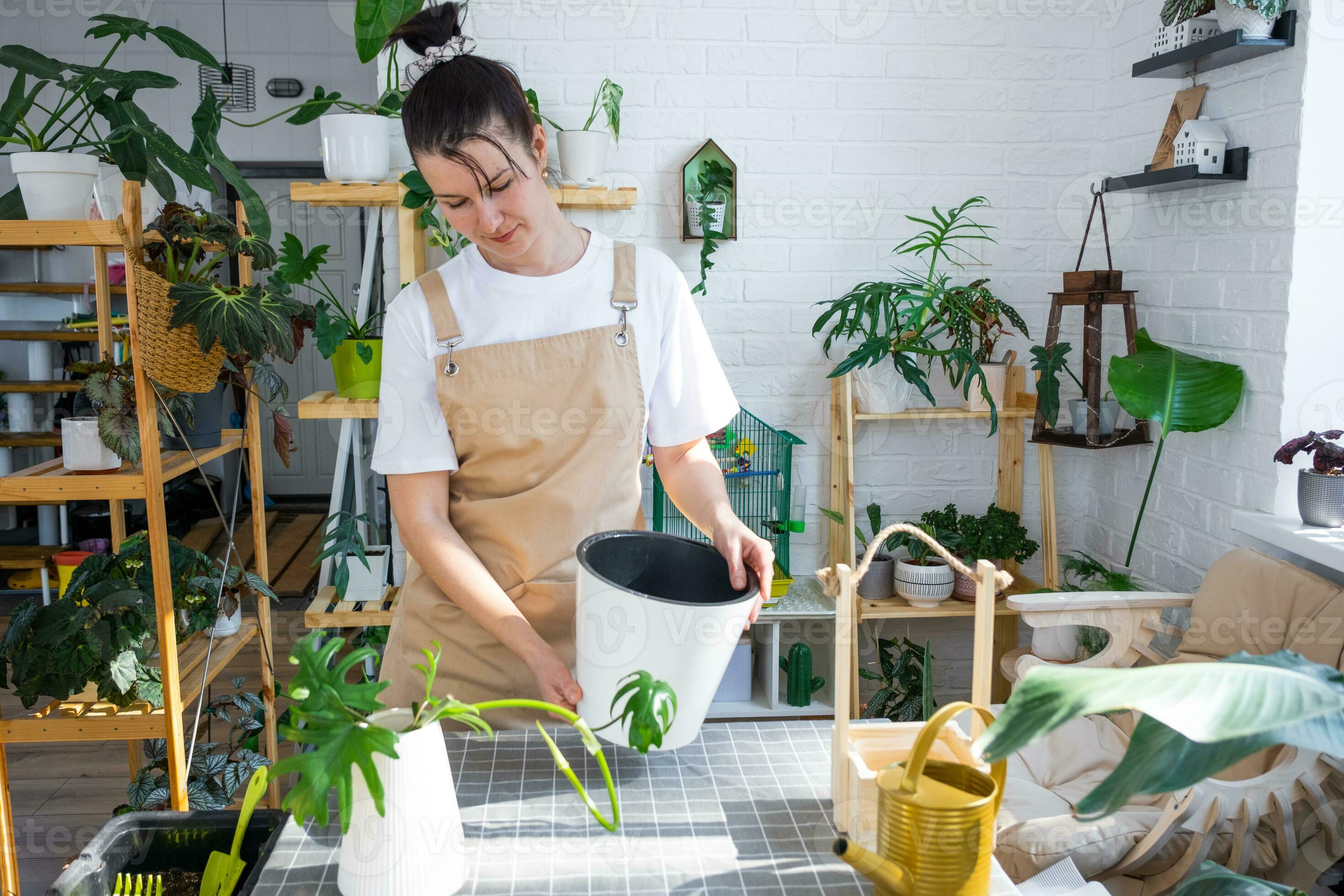 Woman in an apron holds a pot with a double bottom and automatic watering for planting rooted ...