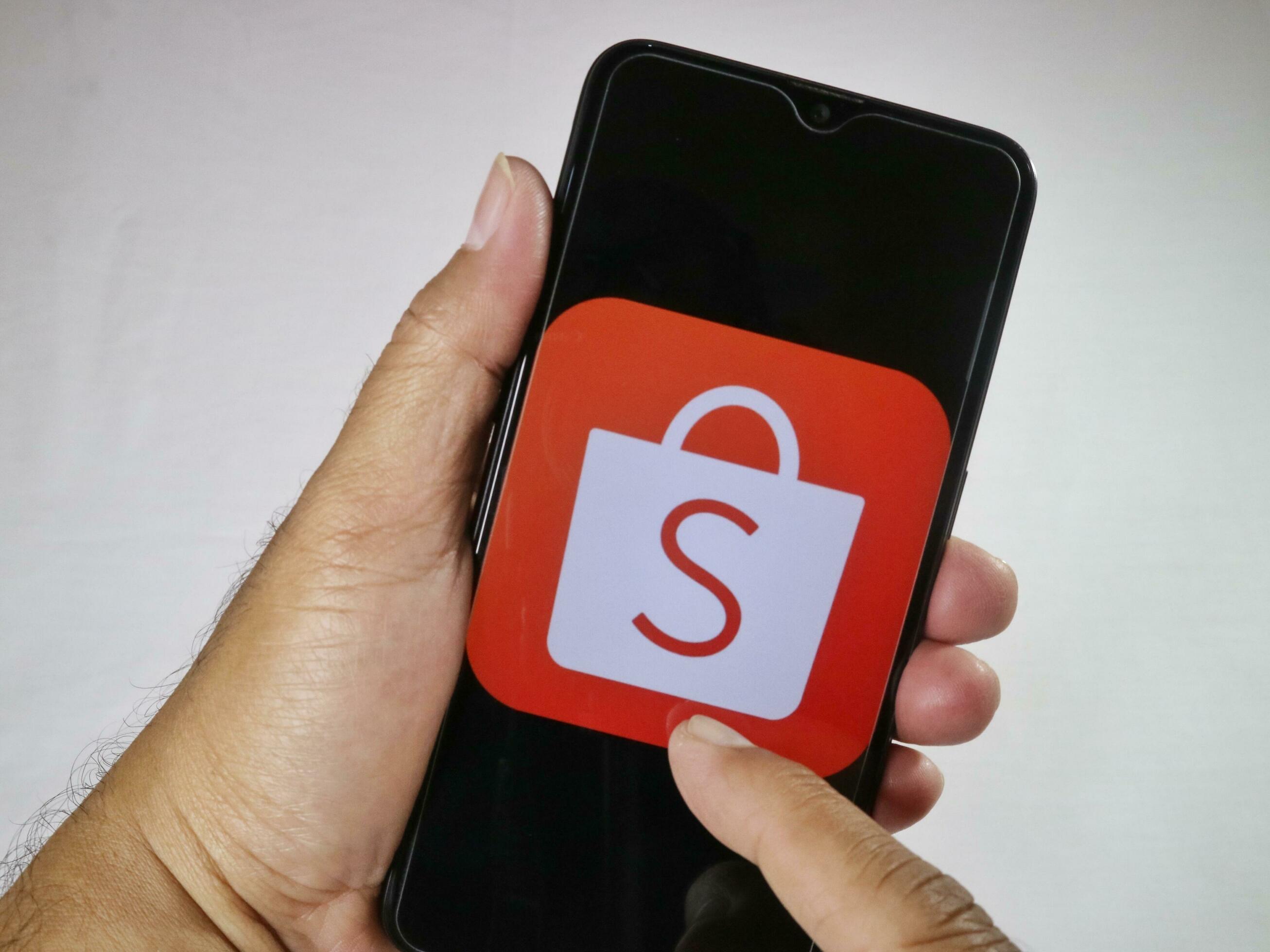 Jakarta, Indonesia, 2023. Hand holding mobile phone with finger touch the Shopee logo on screen ...