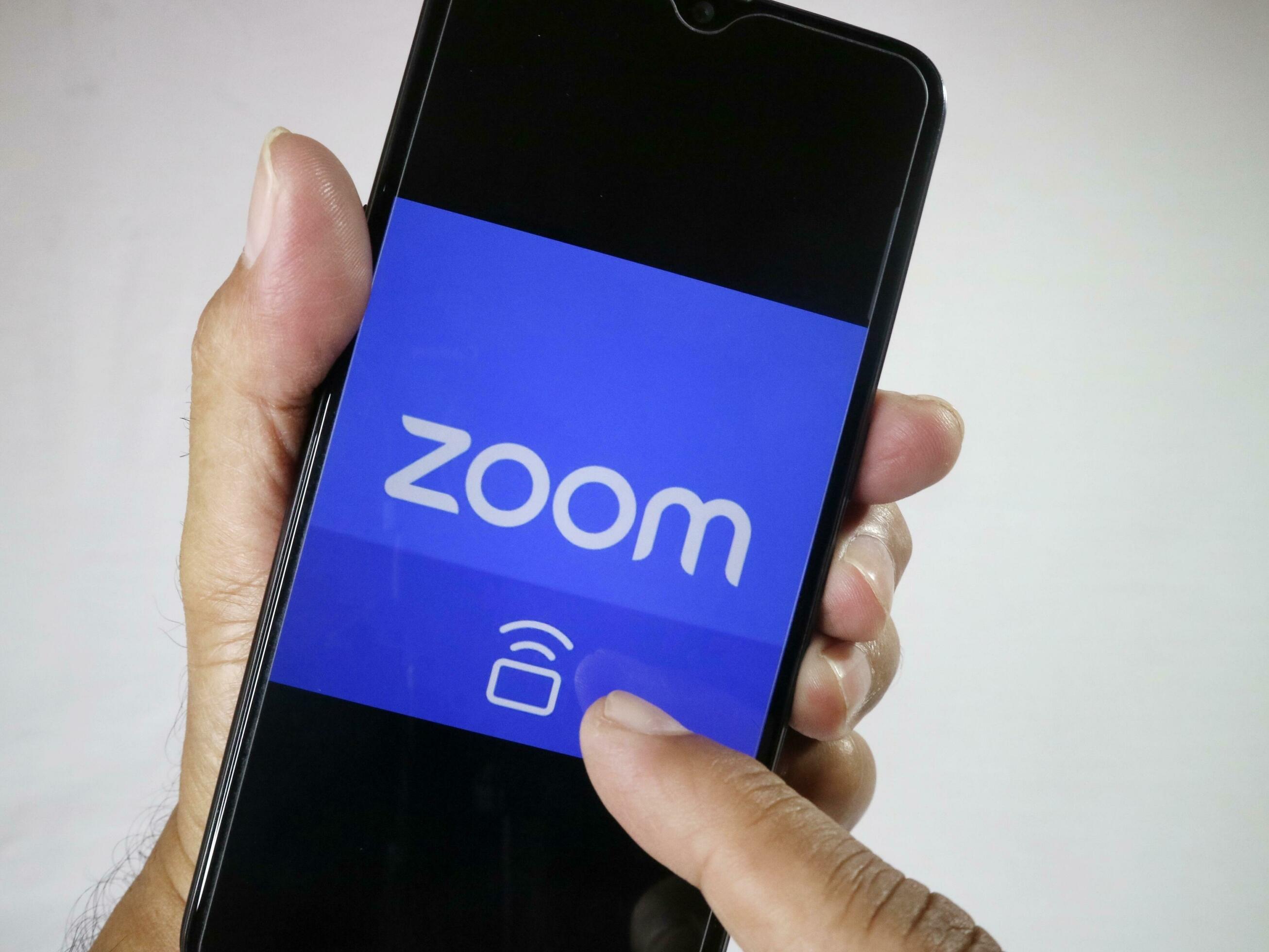 Jakarta, Indonesia, 2023. Hand holding mobile phone with finger touch the ZOOM logo on screen ...