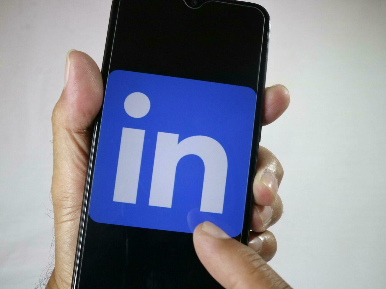 Jakarta, Indonesia, 2023. Hand holding mobile phone with finger touch the Linkedin logo on ...