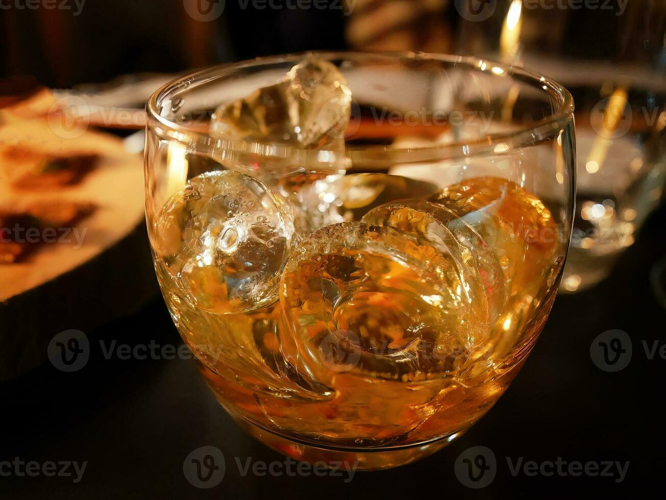 Liquor glass with ice on dark table, yellow amber alcoholic beverage. Whiskey, single malt ...
