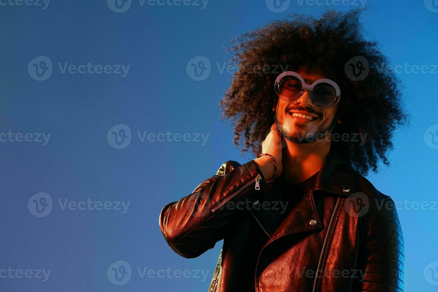 Portrait of a stylish man with curly hair with glasses smile on blue ...