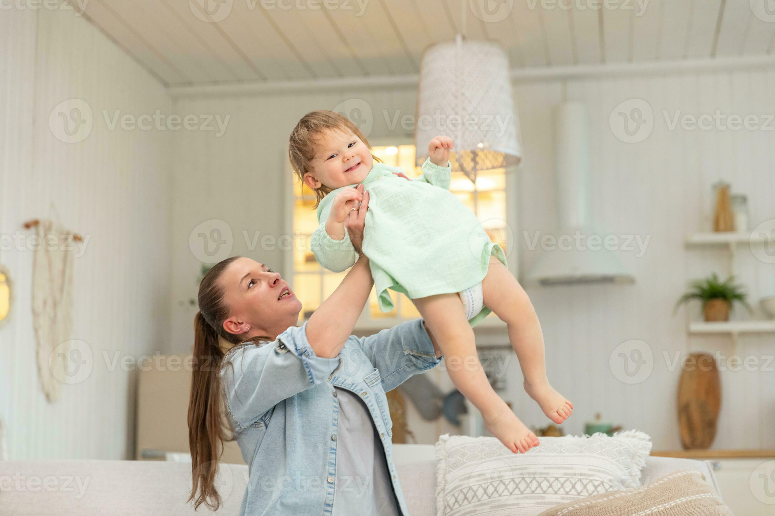 Happy family at home. Mother lifting in air little toddler child daughter. Mom and baby girl ...