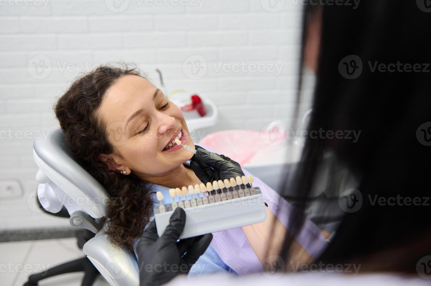 Dentist Placing Tooth Color Chart Over A Smiling Womans Teeth