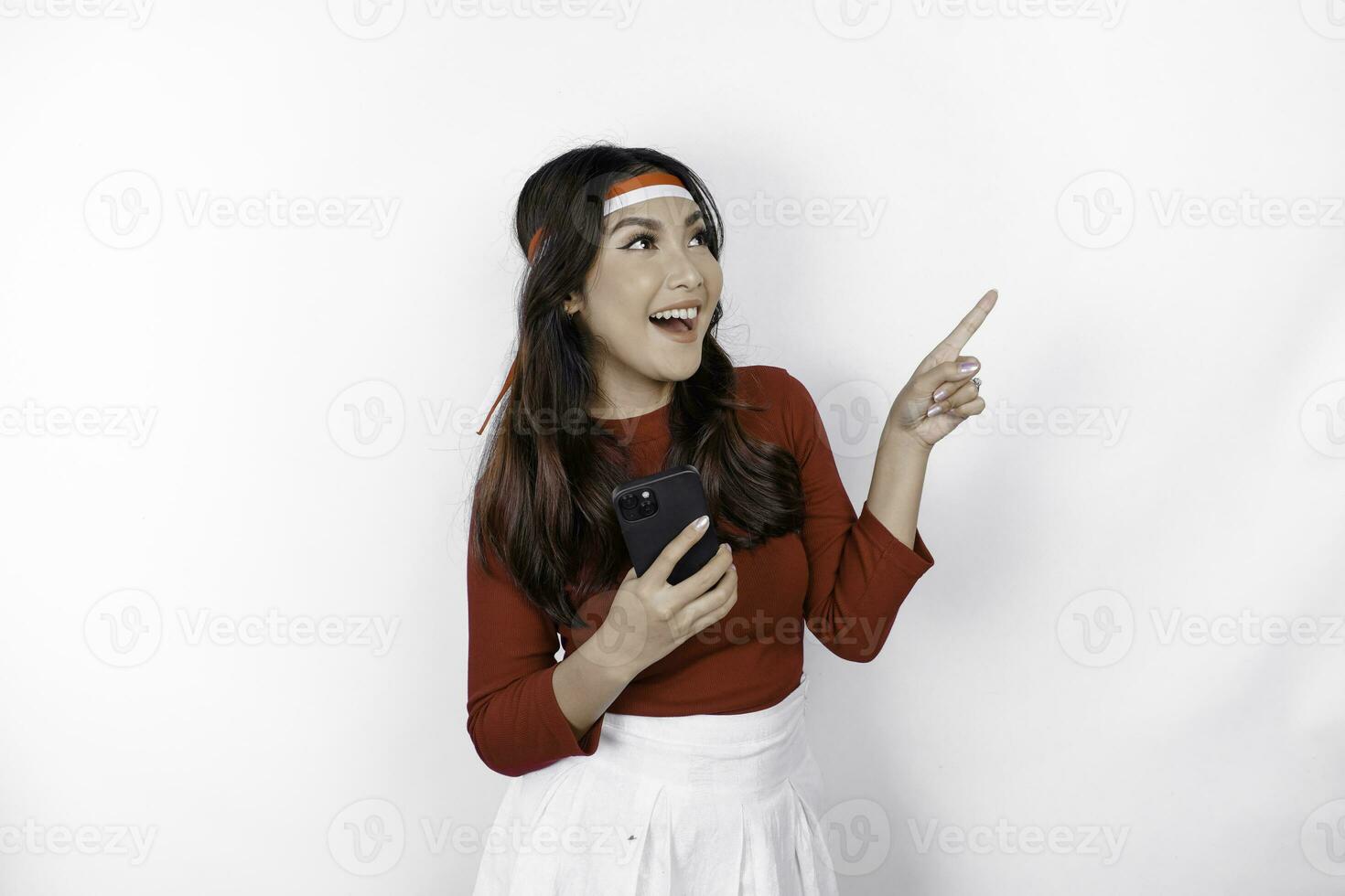 A Happy Asian Woman Wearing Headband Holding Her Phone And Pointing