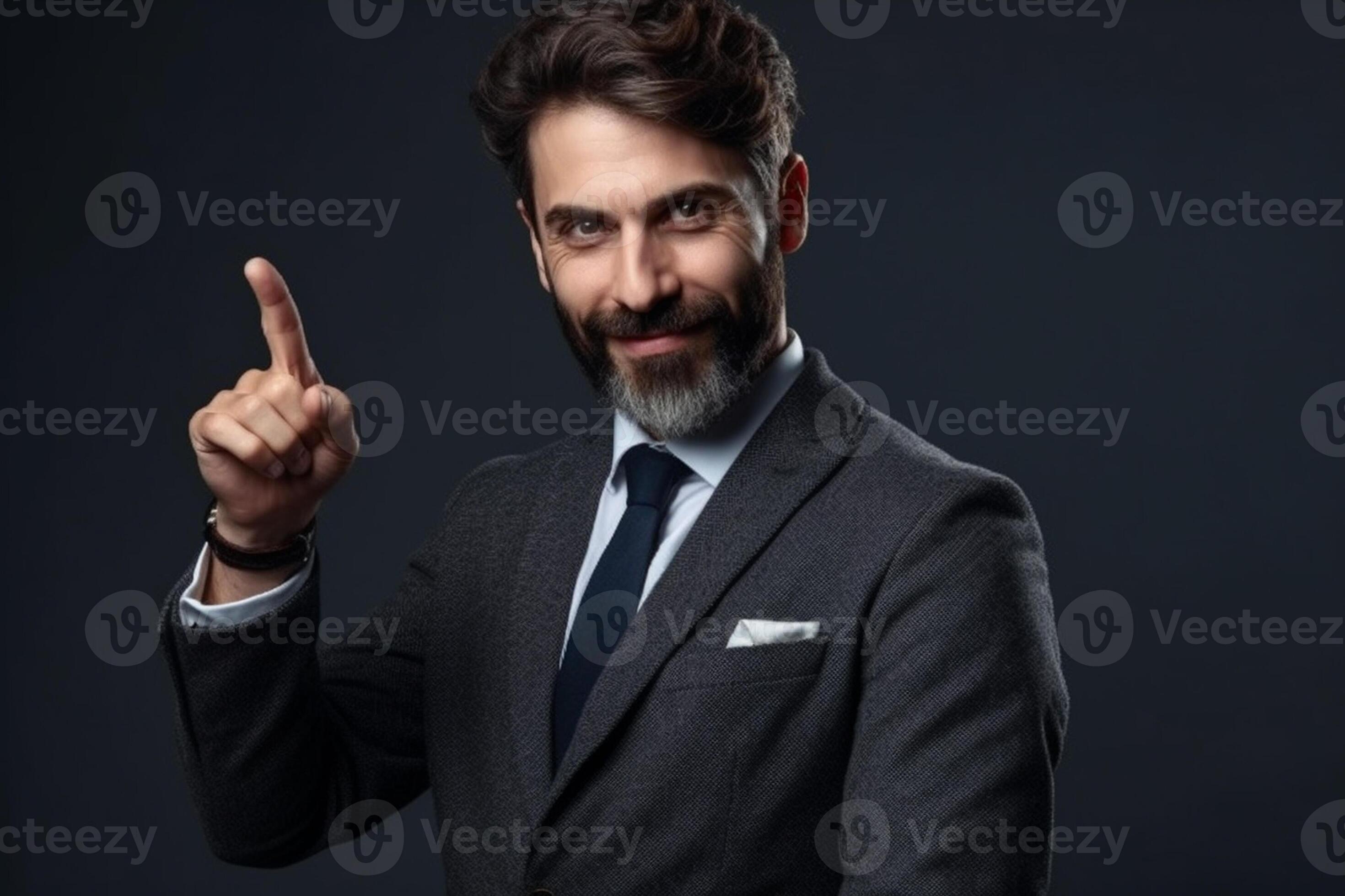 Cheerful young man in suit pointing at camera with index finger ...