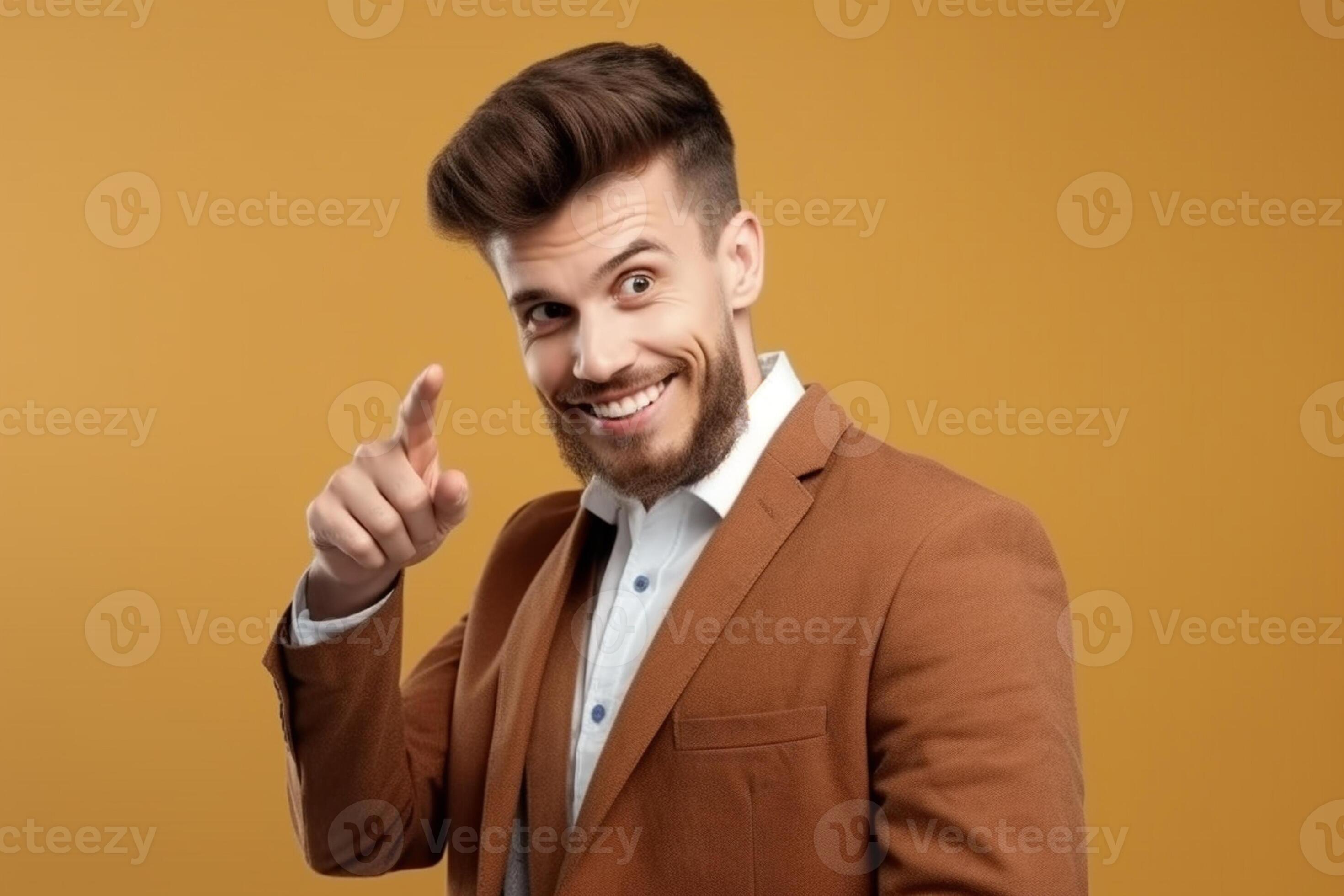 Cheerful young man in suit pointing at camera with index finger ...