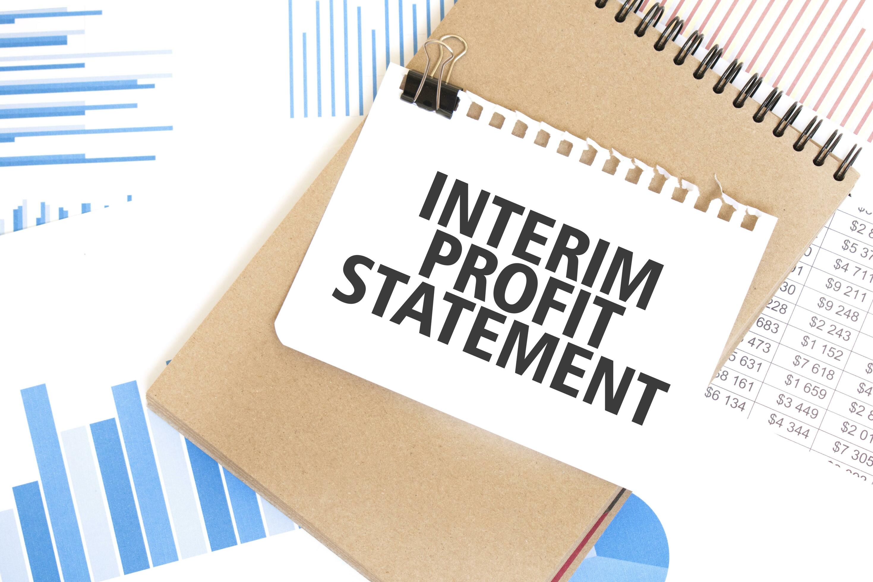 Text INTERIM PROFIT STATEMENT on white paper sheet and brown paper notepad on the table with ...