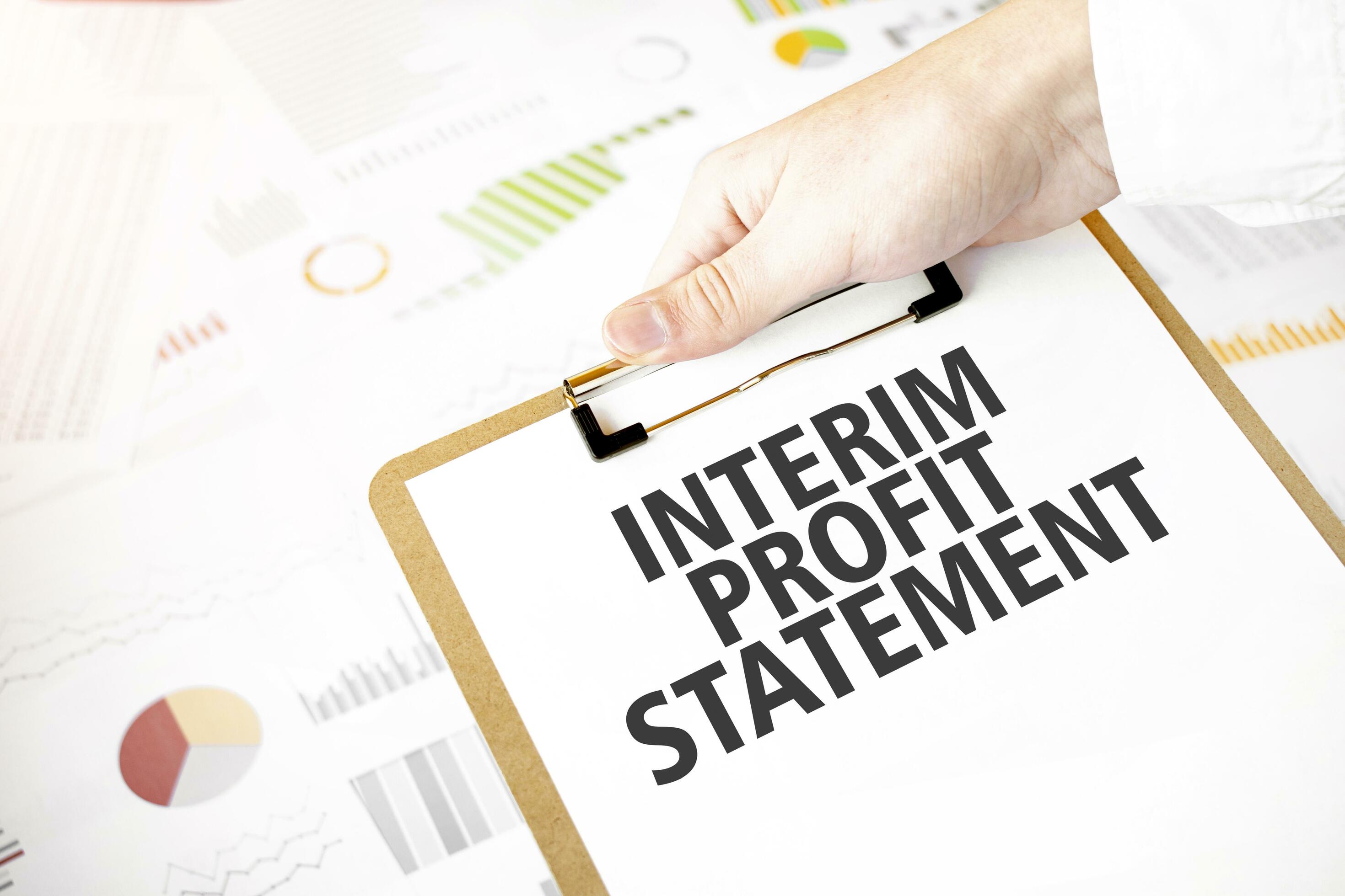 Text INTERIM PROFIT STATEMENT on white paper plate in businessman hands with financial diagram ...