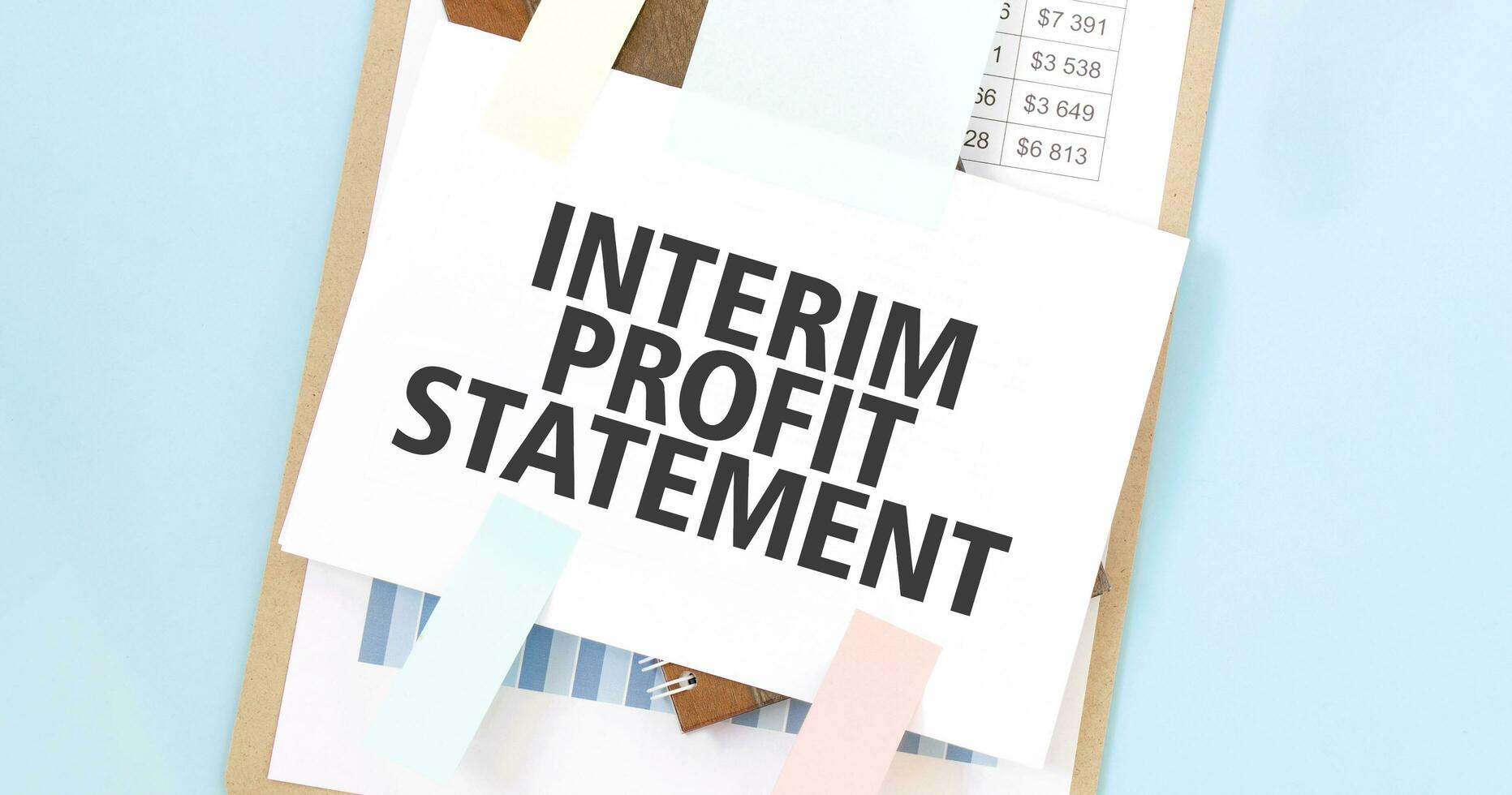 Paper plate with text take INTERIM PROFIT STATEMENT. Diagram, notepad and blue background ...