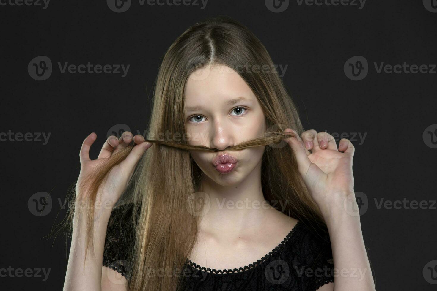 Beautiful teenage girl fooling around in front of the camera. She makes a mustache out of her ...