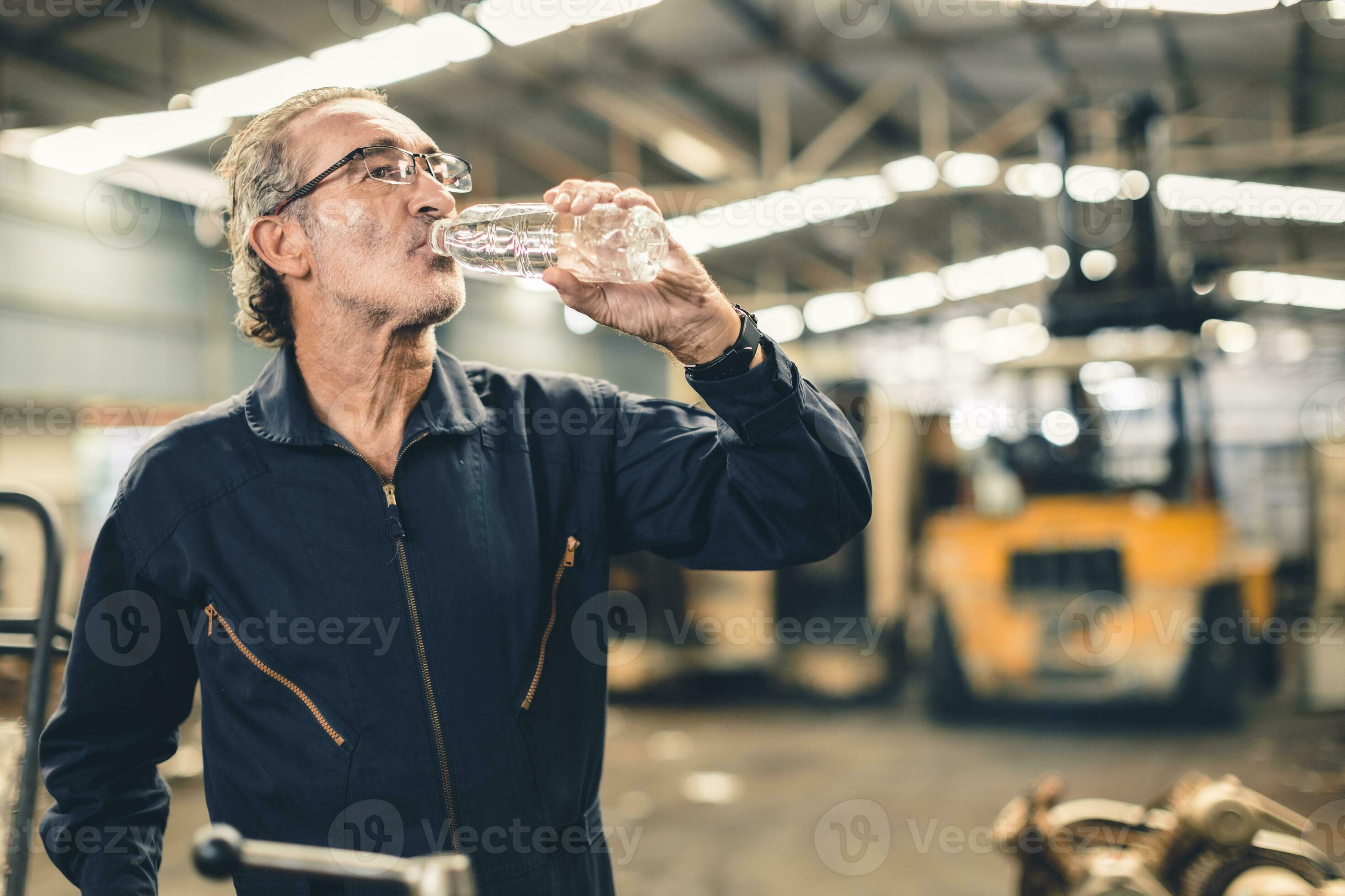Thirsty senior male staff worker drinking water refreshing from tired hard work in hot workplace ...