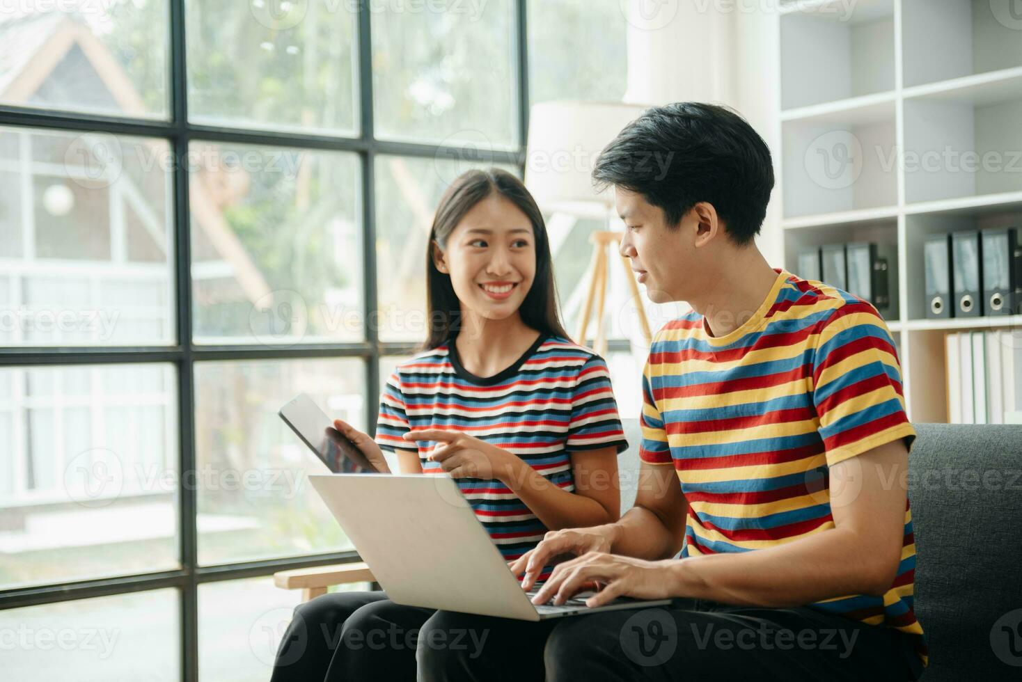 Two asian students learning together online with a laptop, tablet and tutor together in living ...