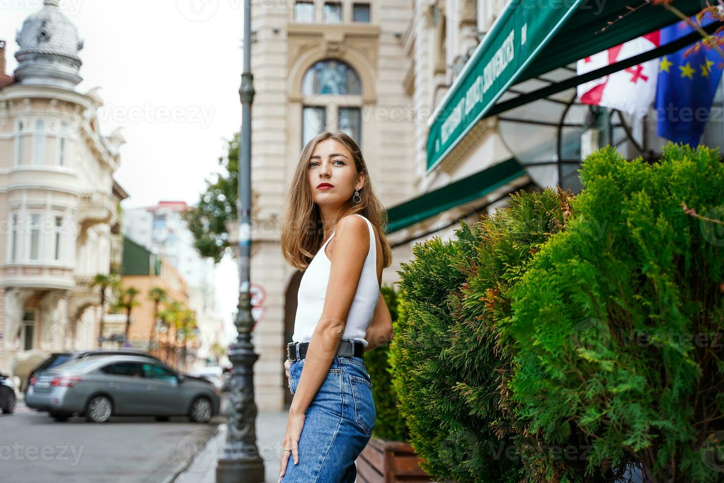 City walk. Young woman standing on sidewalk. Historic building facade near. Beautiful girl ...