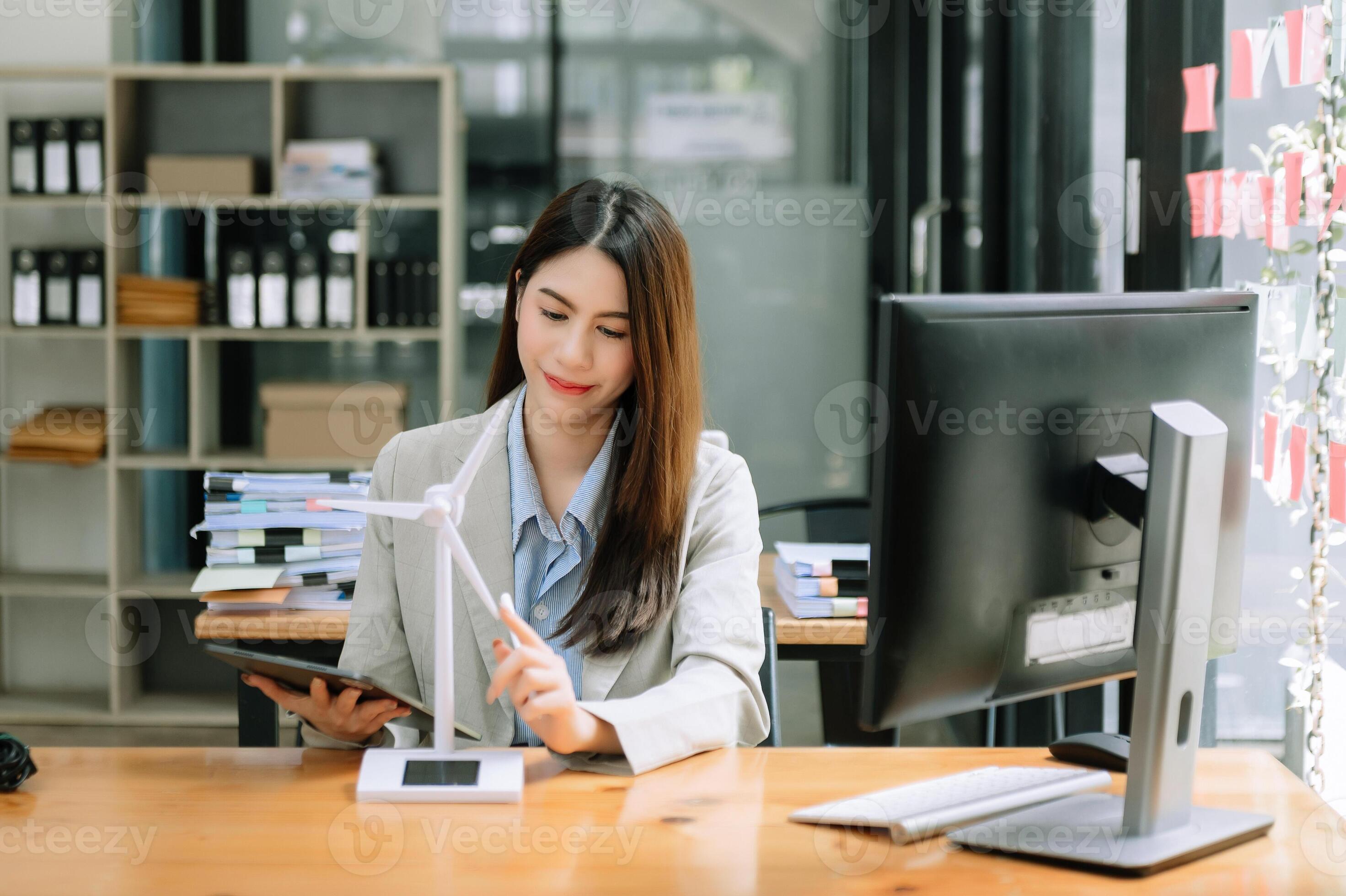Female alternative energy engineer hold a windmill power sample model and discuss with colleague ...