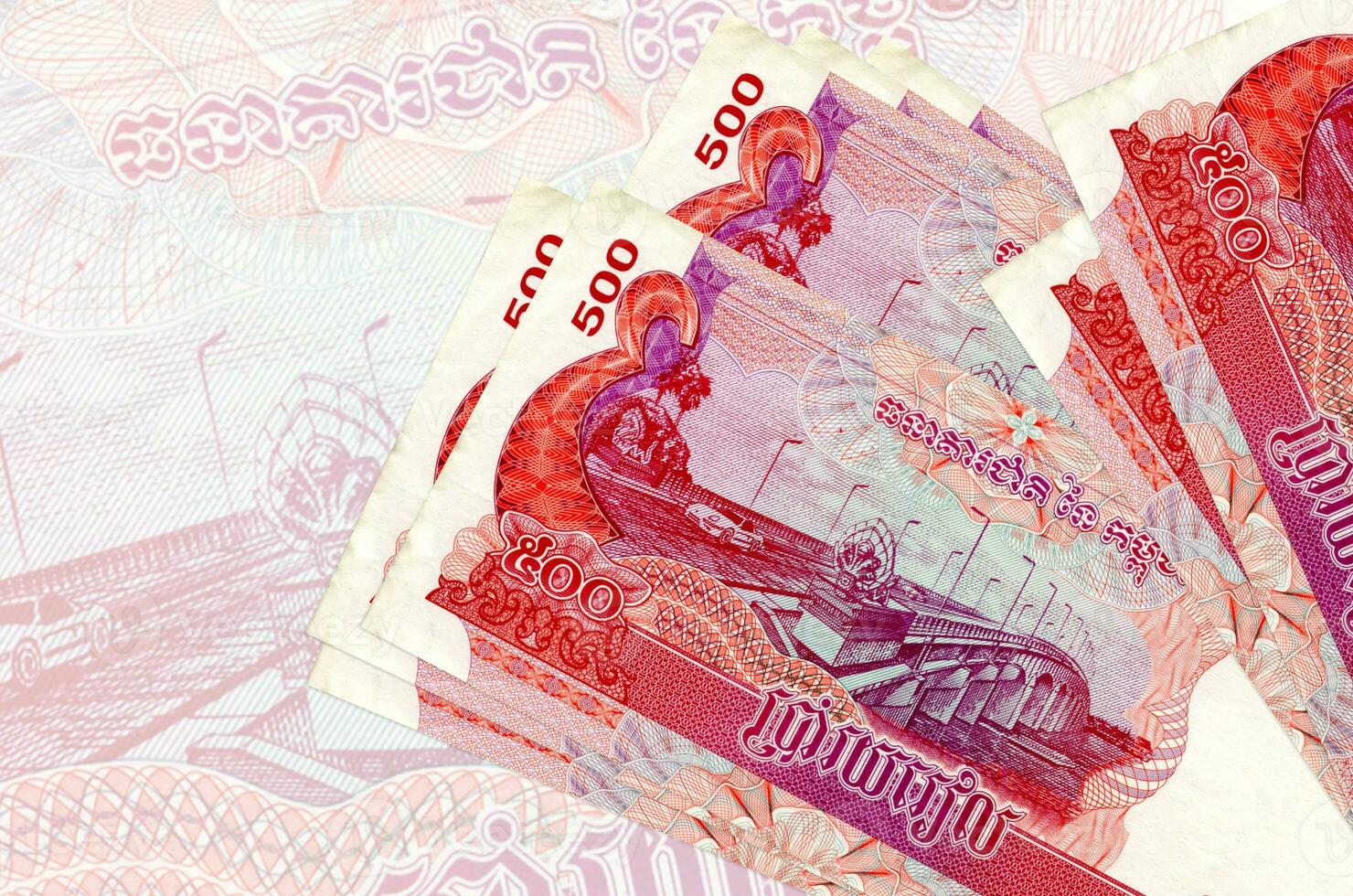 500 Cambodian riels bills lies in stack on background of big semi-transparent banknote. Abstract ...