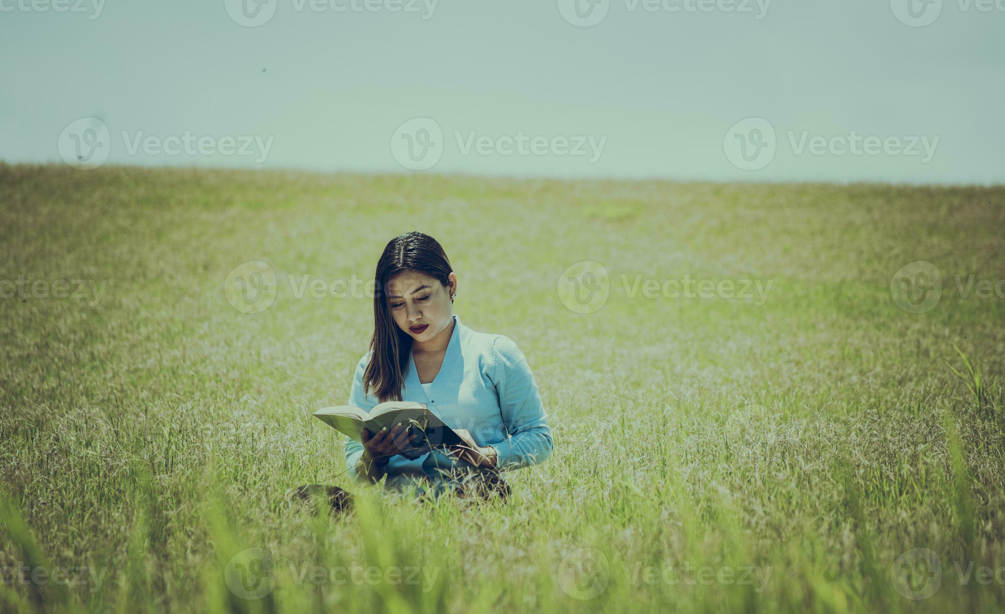 A girl reading a book in the field, A person sitting on the grass reading a book, Attractive ...