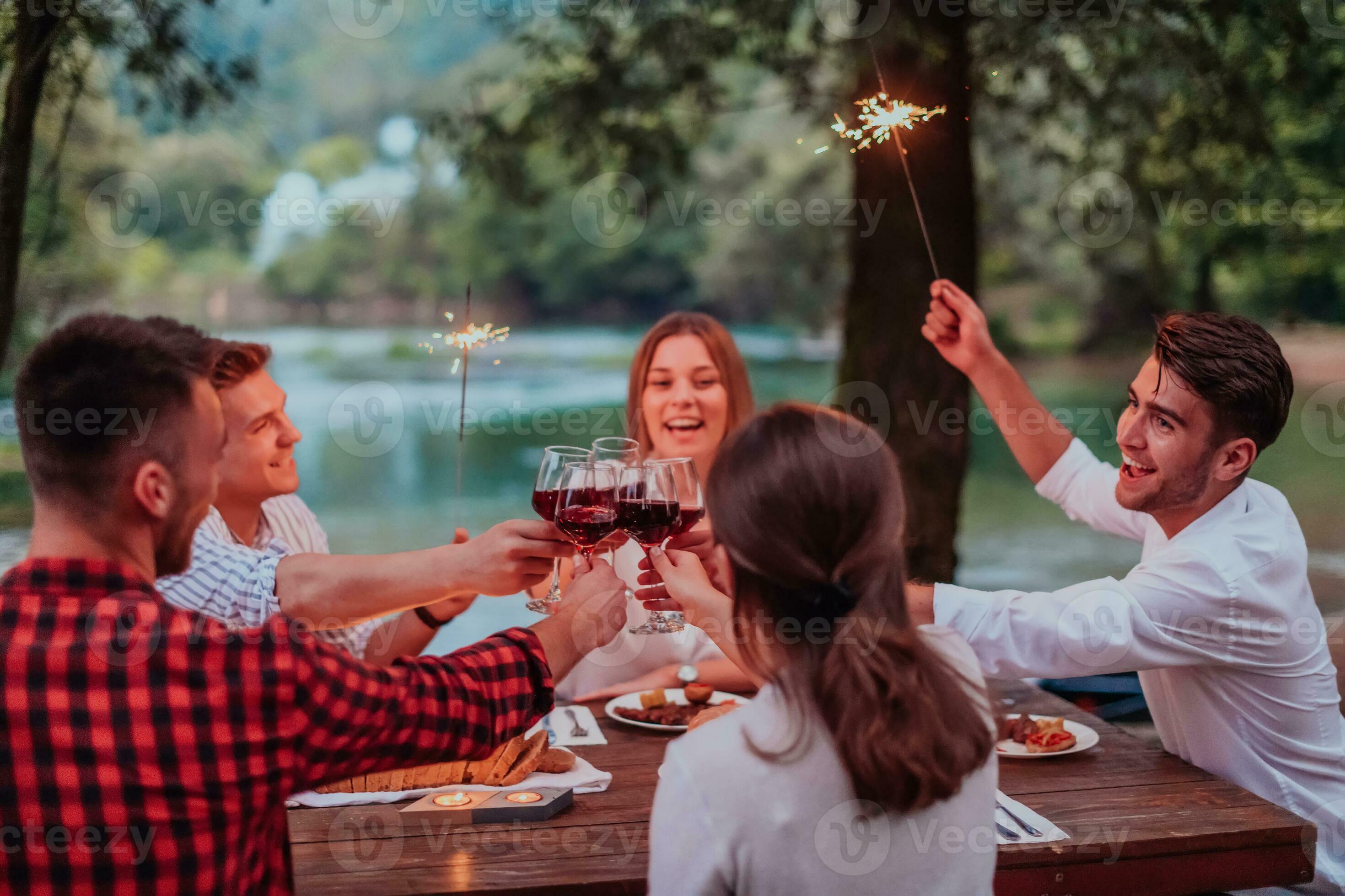 Group of happy friends celebrating holiday vacation using sprinklers and drinking red wine while ...