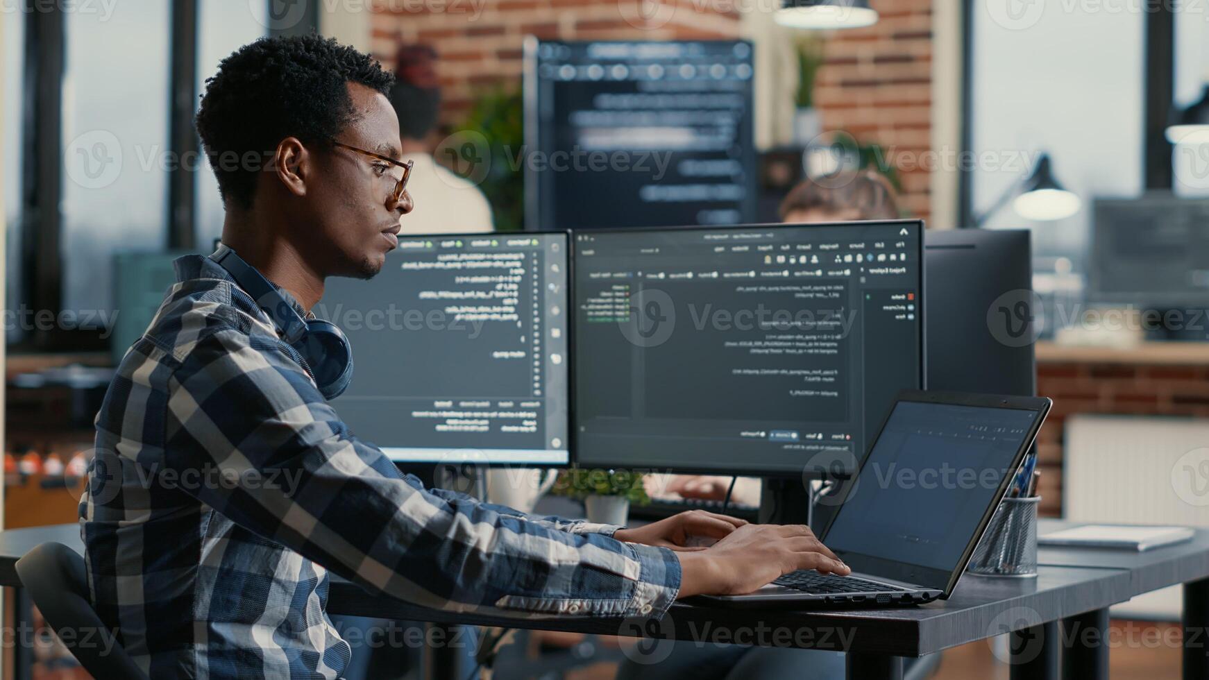 Portrait Of African American Developer Using Laptop To Write Code Sitting At Desk With Multiple