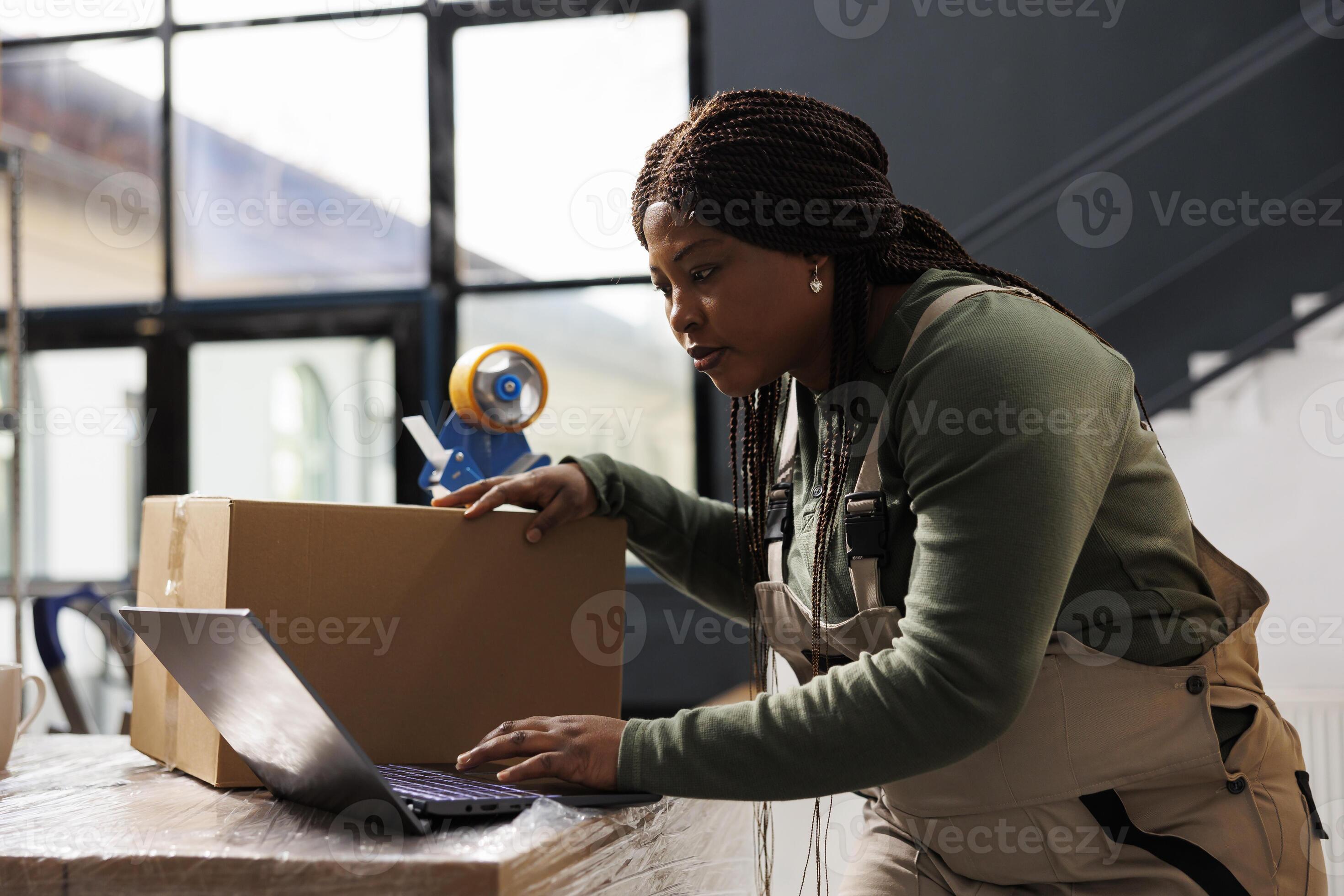 Warehouse manager checking online orders on laptop computer, analyzing shipping details while ...