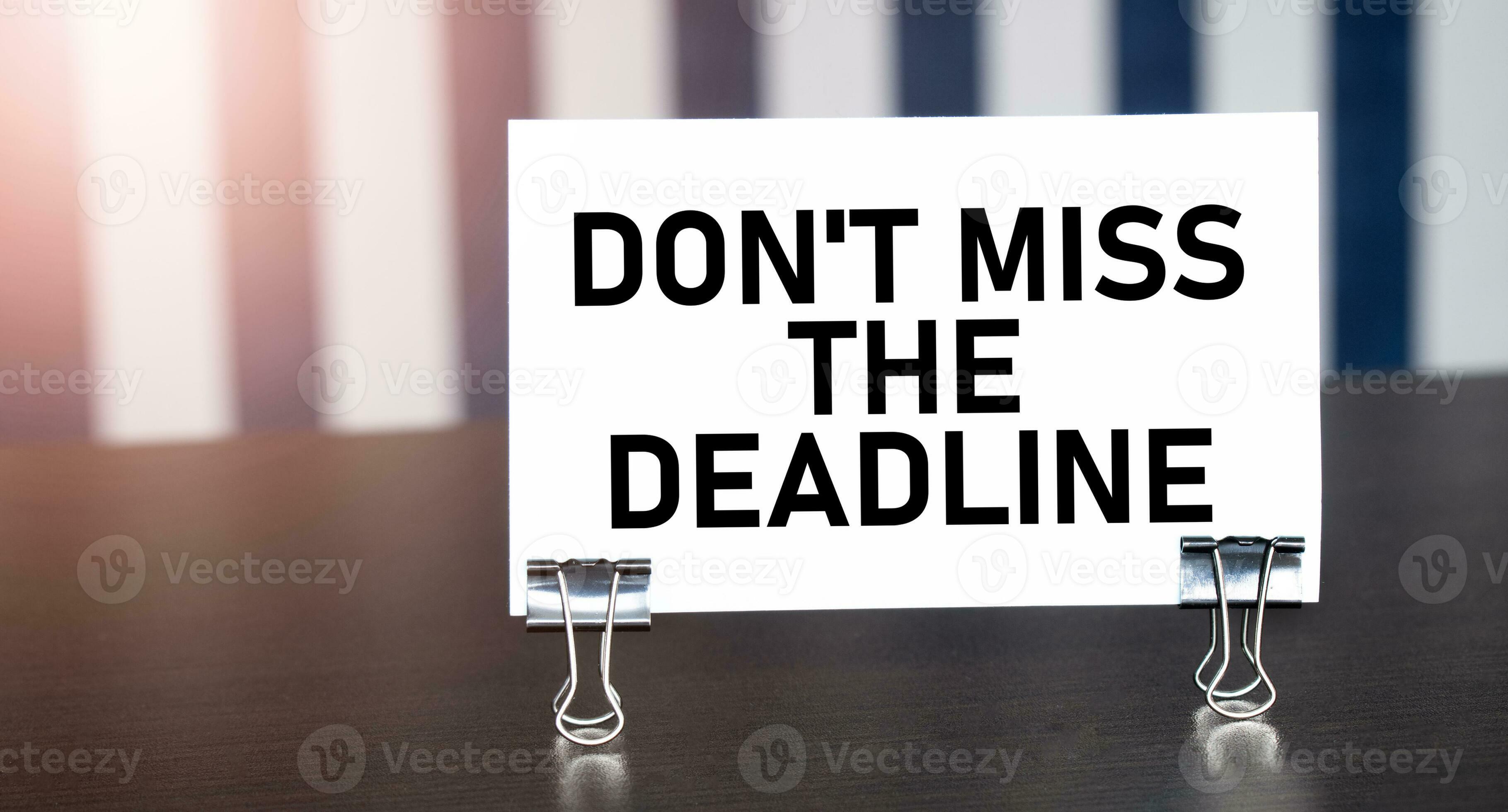 don't miss the deadline sign on paper on dark desk in sunlight. Blue and white background ...