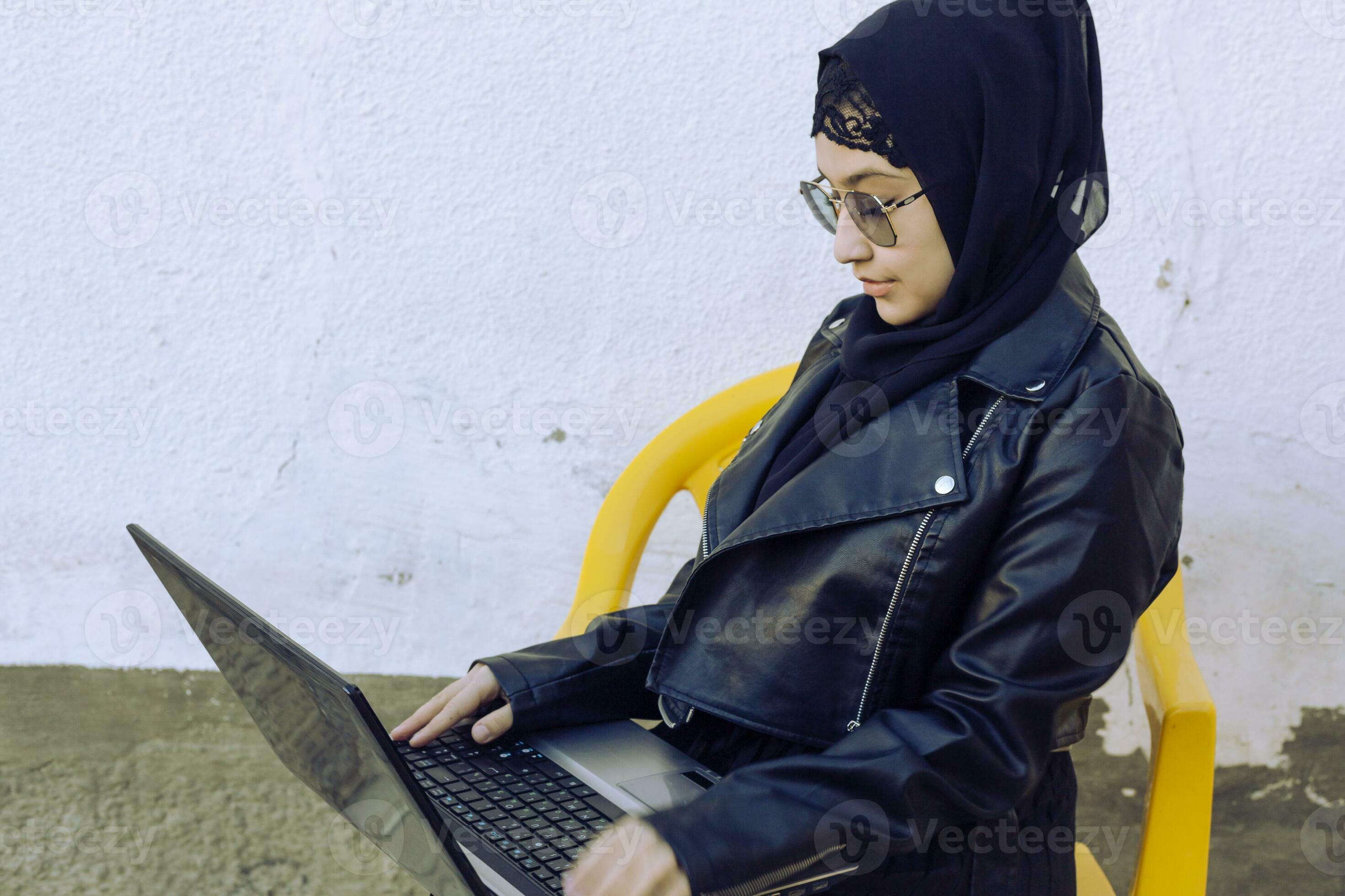 Beautiful middle-eastern working with the laptop. Cute Arabian Muslim woman in hijab posing with ...