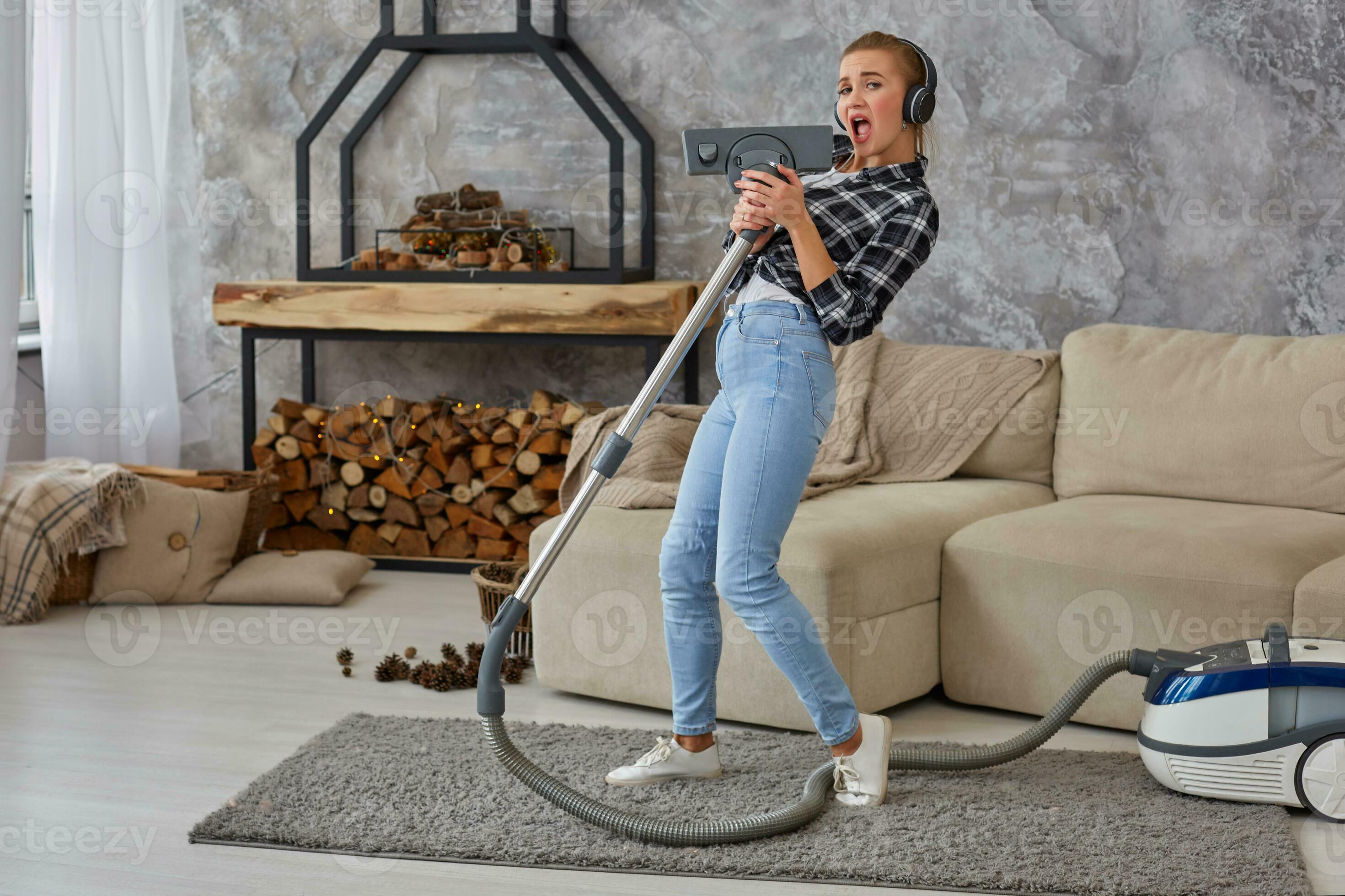 Cheerful young woman enjoying solo singing with vacuum cleaner while cleaning house 35178725 ...