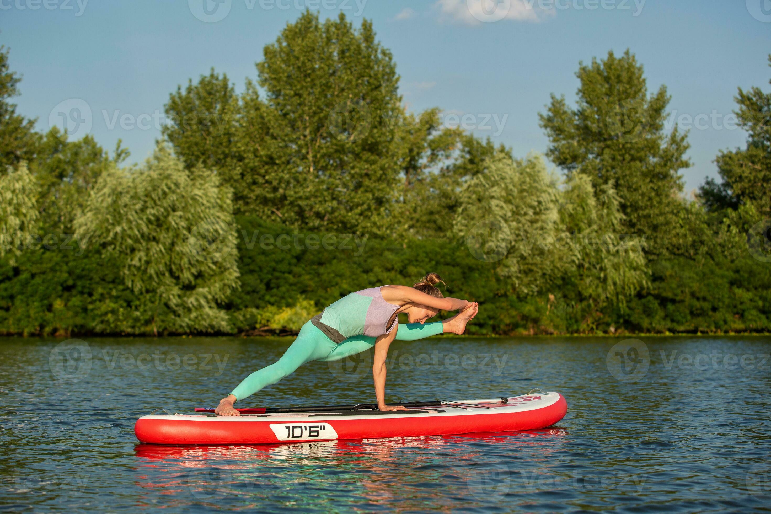Young woman doing yoga on sup board with paddle. Yoga pose, side view - concept of harmony with ...