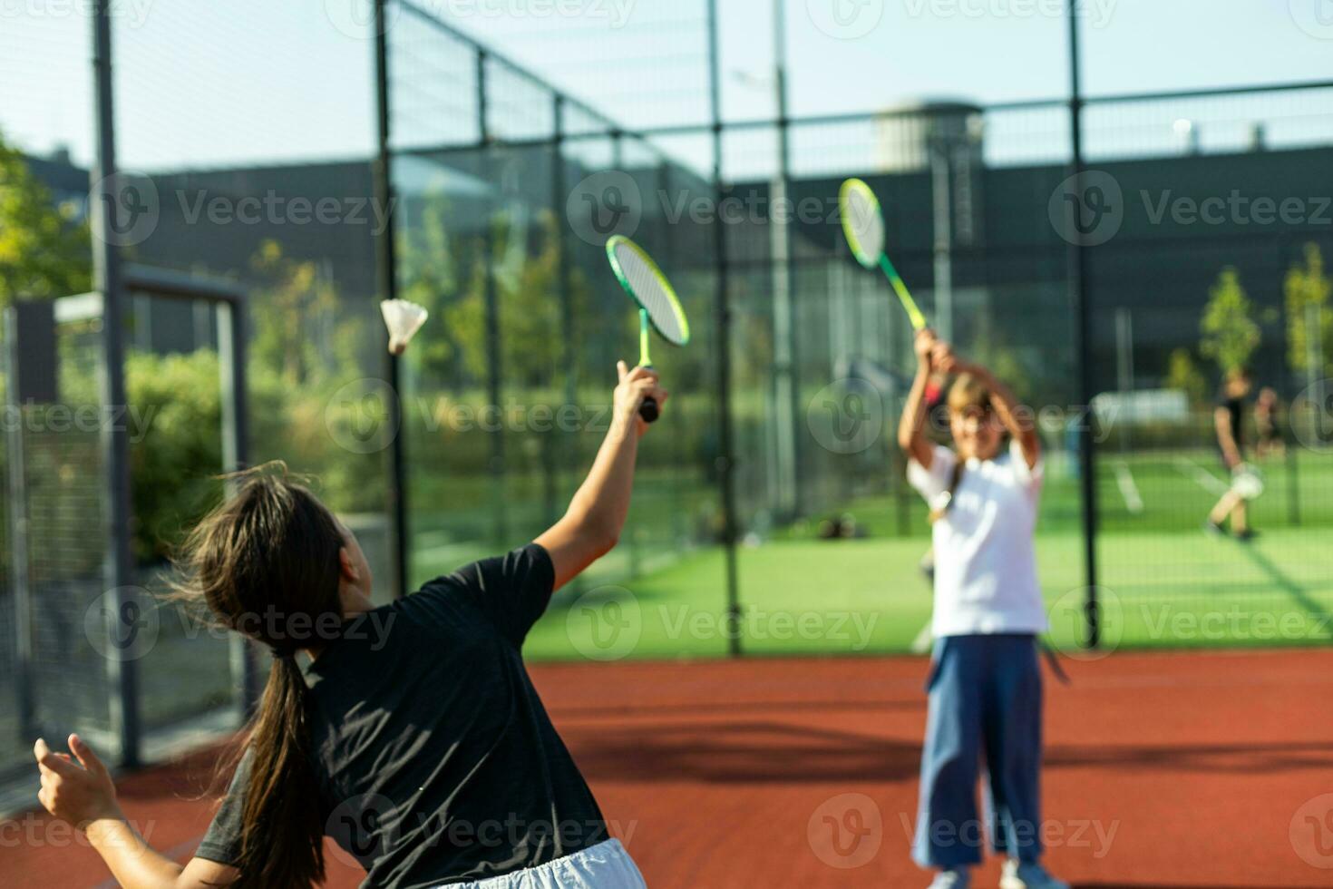 Happy sporty elementary school age girl, child playing badminton, holding a racket making funny ...