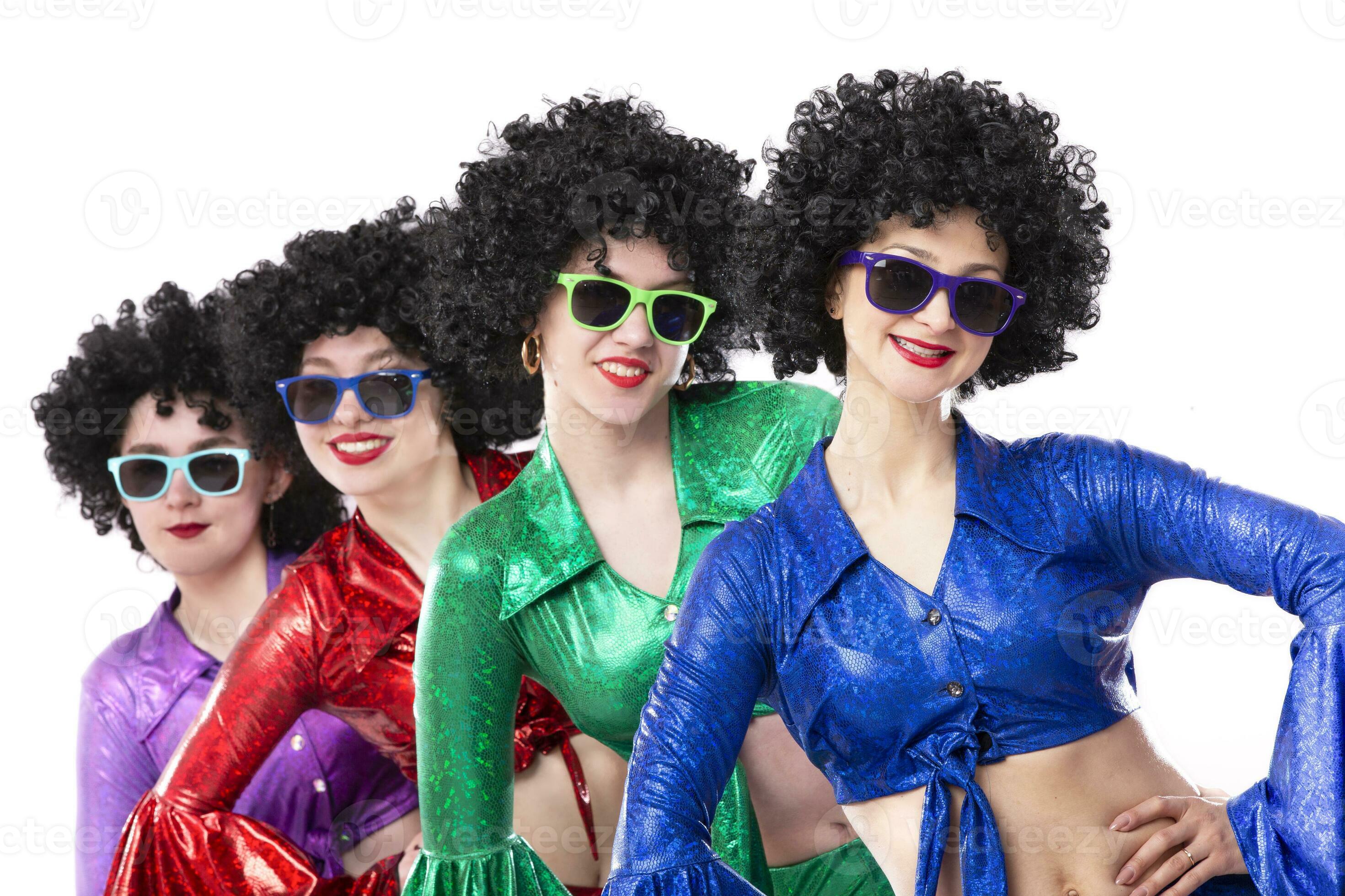 A group of girls in disco style and African wigs in colorful costumes on a white background ...