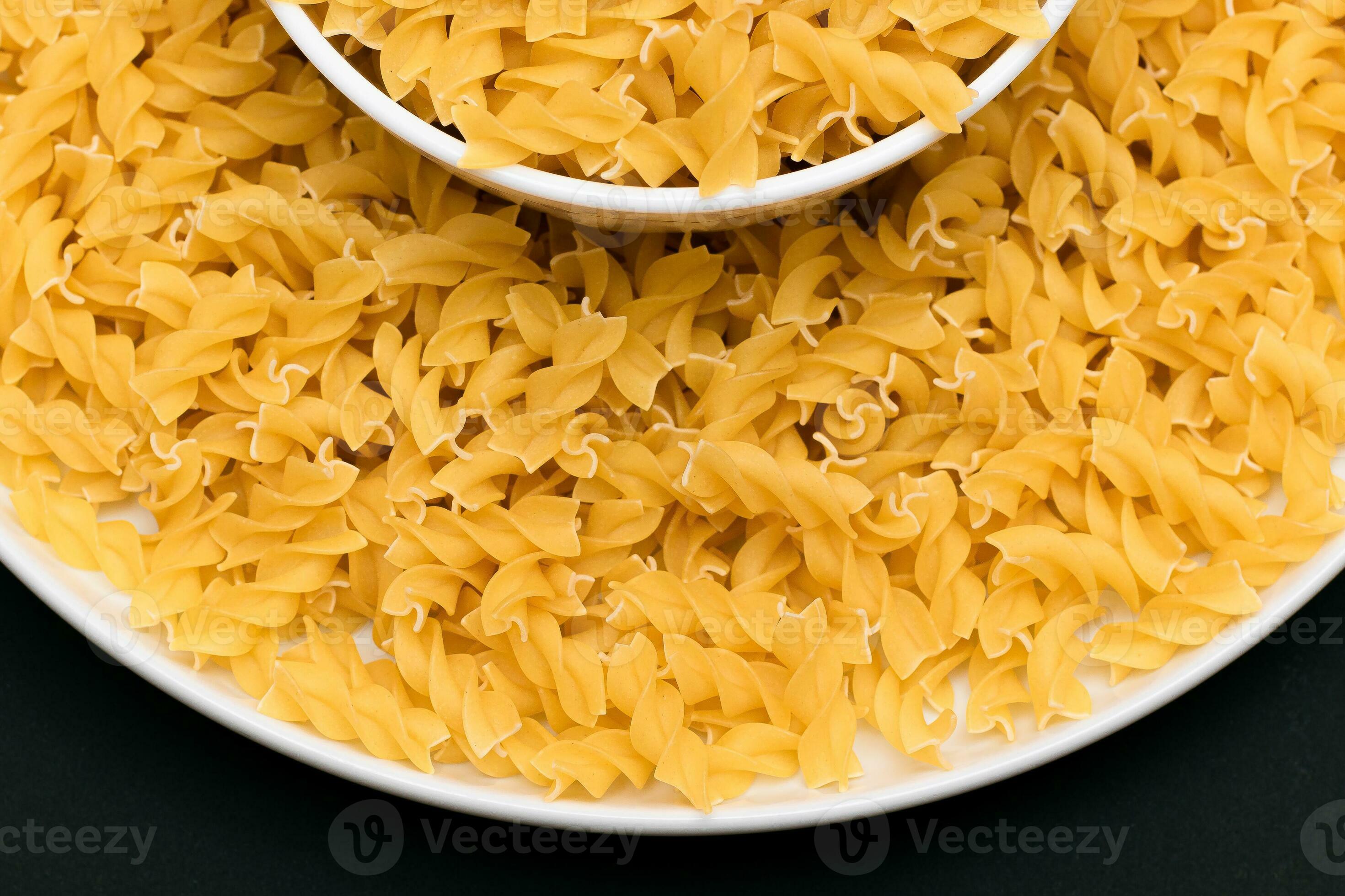 Uncooked Fusilli Pasta Lying on White Plate on Black Background. Raw and Dry Macaroni. Unhealthy ...