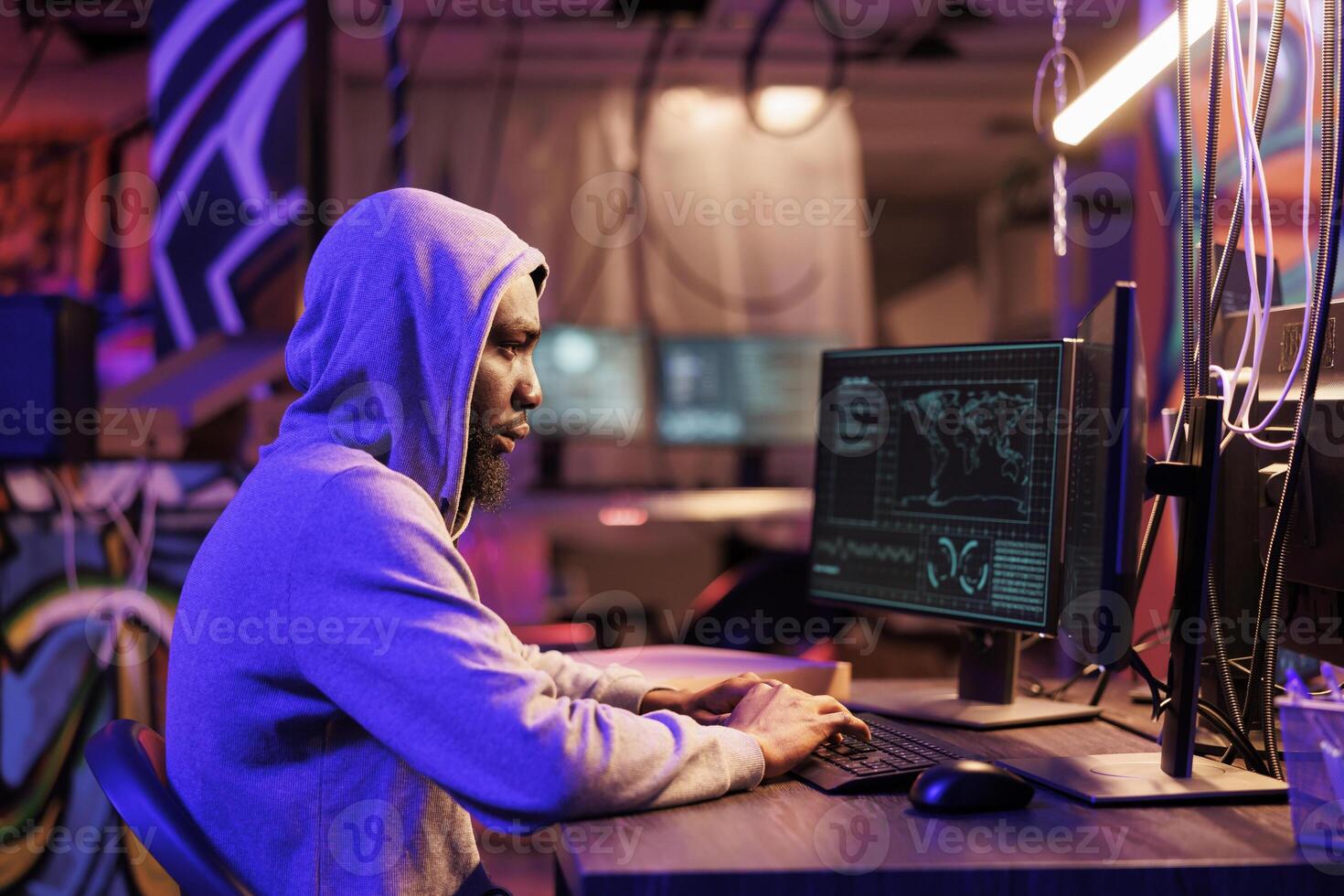 African American Hacker Coding Spyware In Abandoned Warehouse Man In Hood Using Computer For