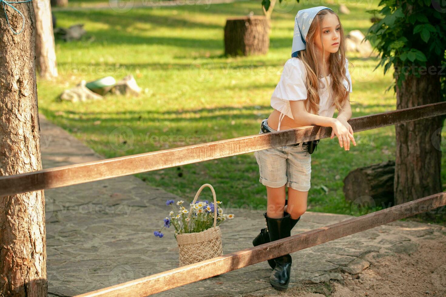 Teenage girl leaning on iron fence while walking in summer country park ...