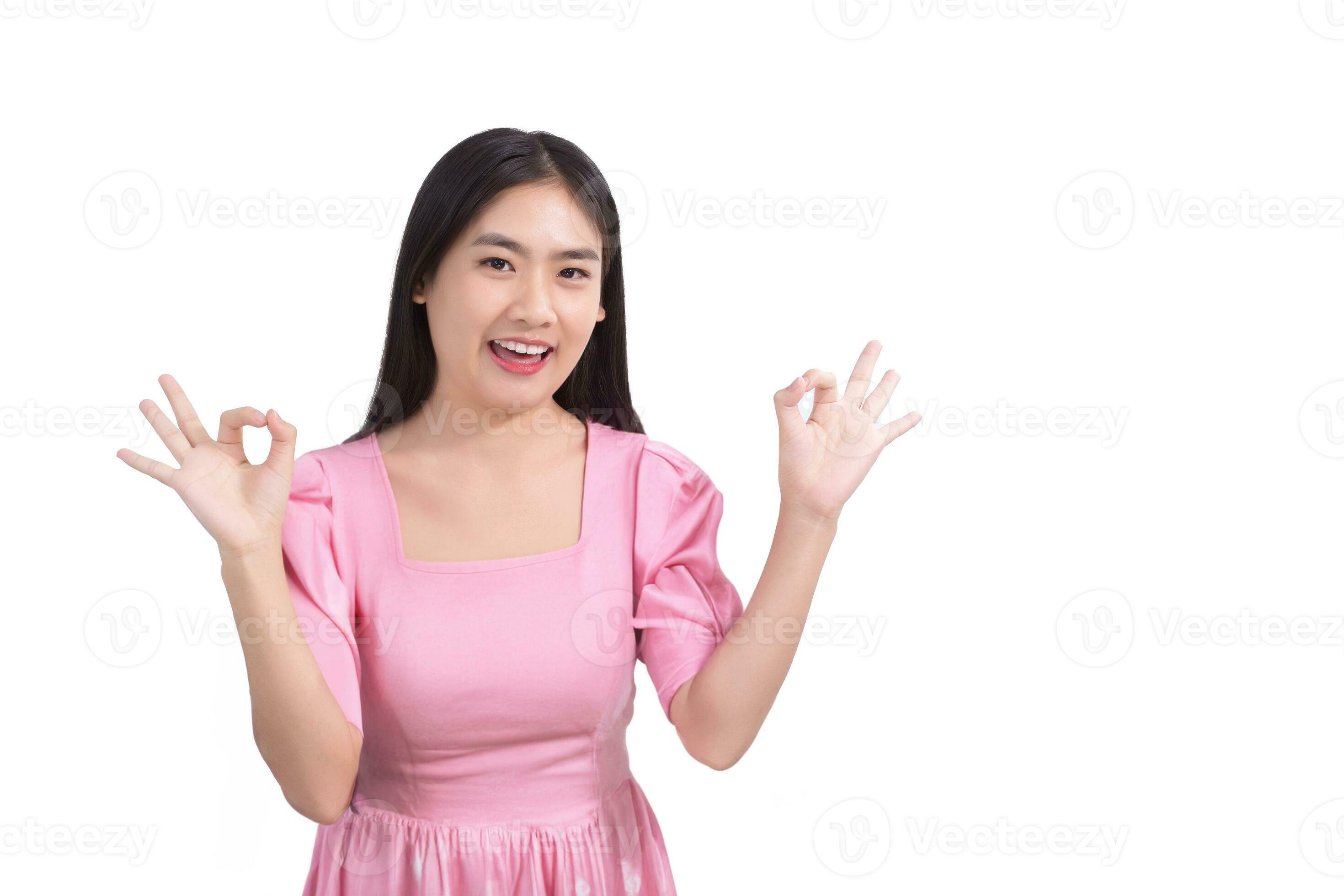 Pretty young Asian woman with long black hair wears pink dress and shows hand okey sign while ...