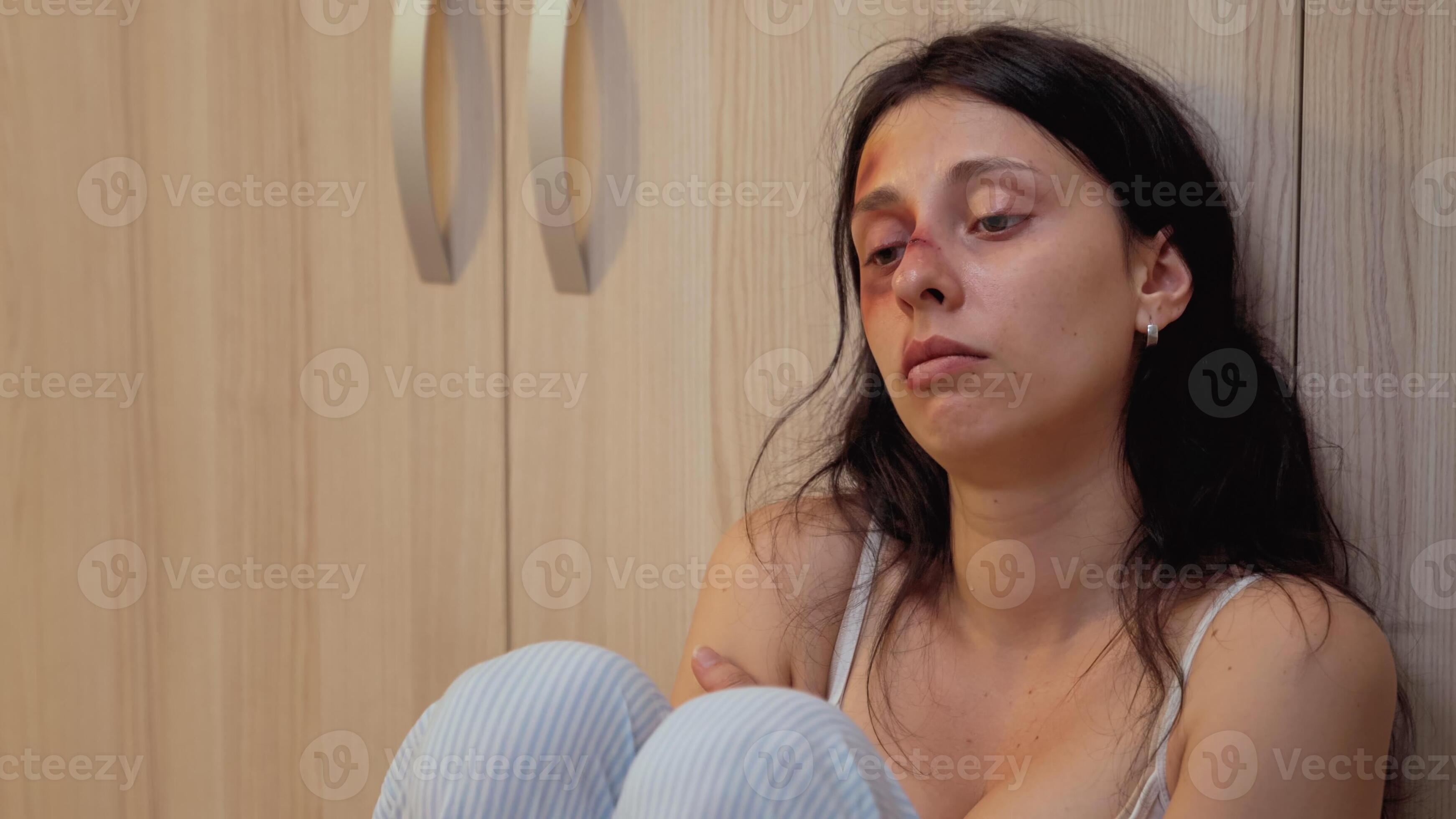 Abused woman sitting on the floor sad and helpless. Traumatised abused terrified beaten wife ...