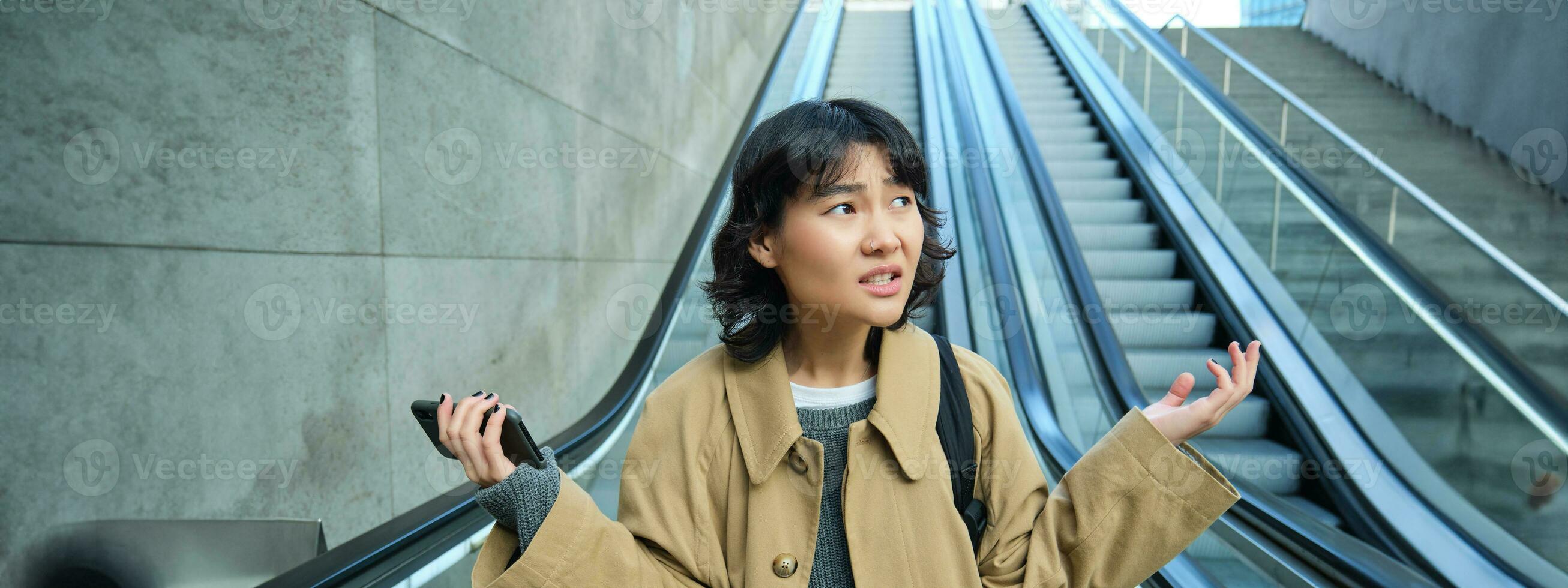 Portrait of confused asian girl doesn't know where she is, lost in unfamiliar city, goes down ...
