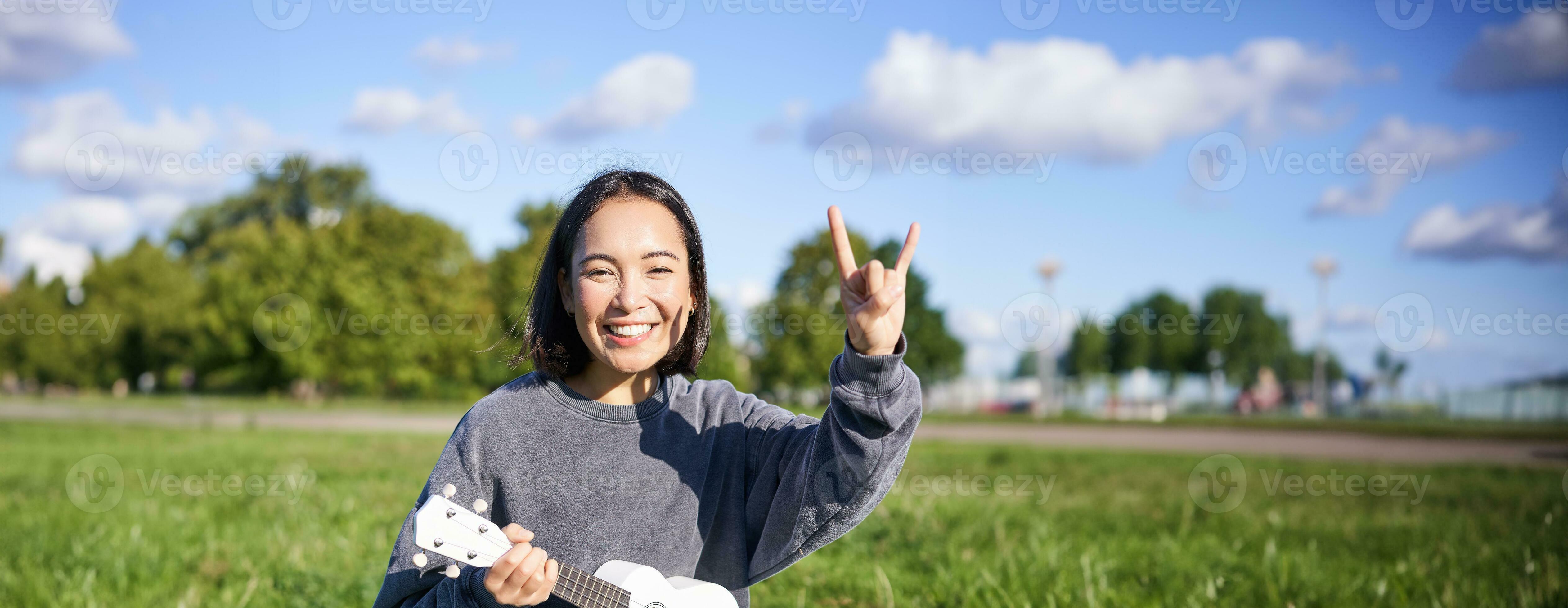 Happy Asian Girl Playing Ukulele In Park Showing Rock N Roll Heavy