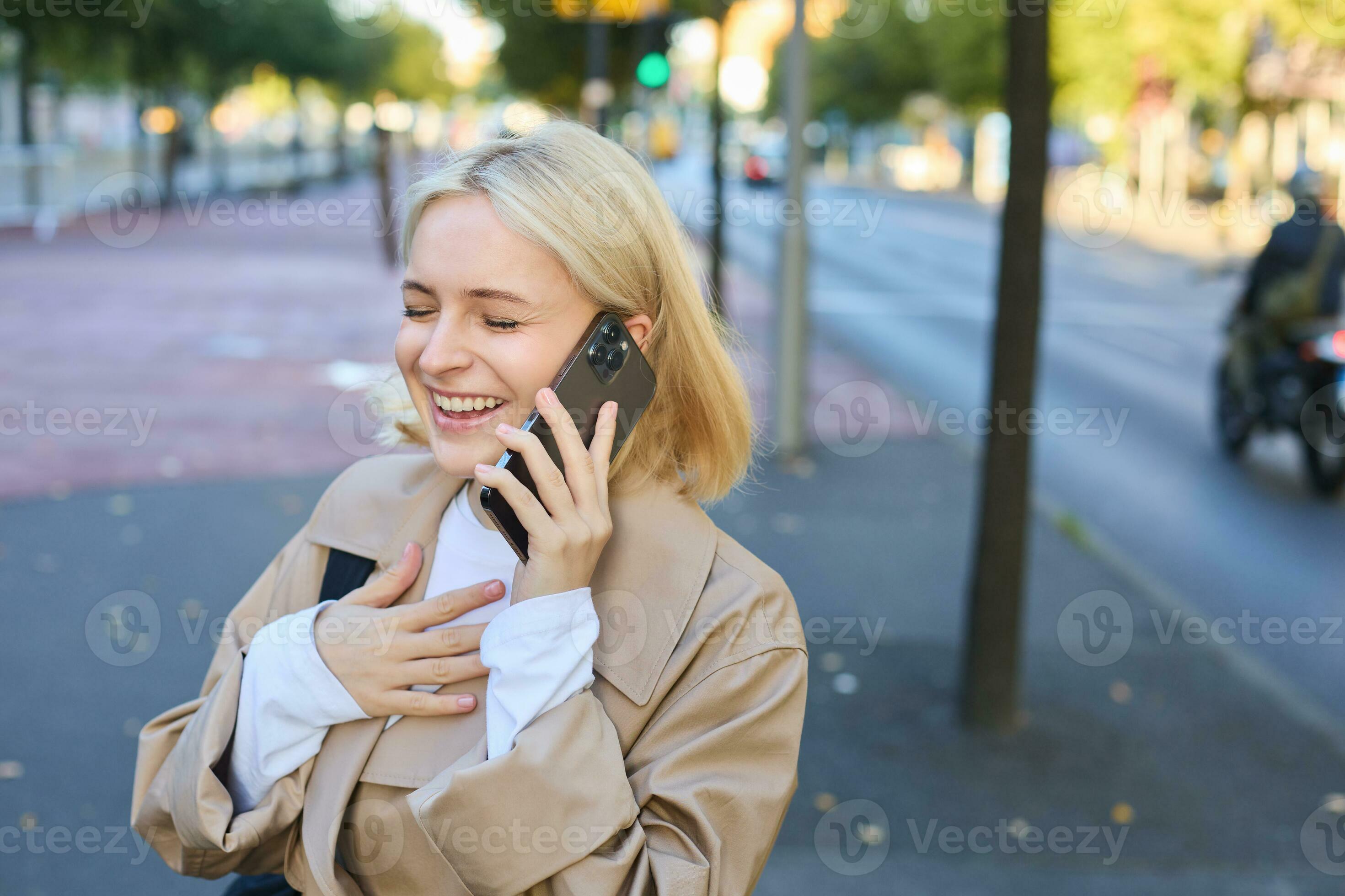 Close up portrait of beautiful young woman, blonge girl walking on street with mobile phone ...