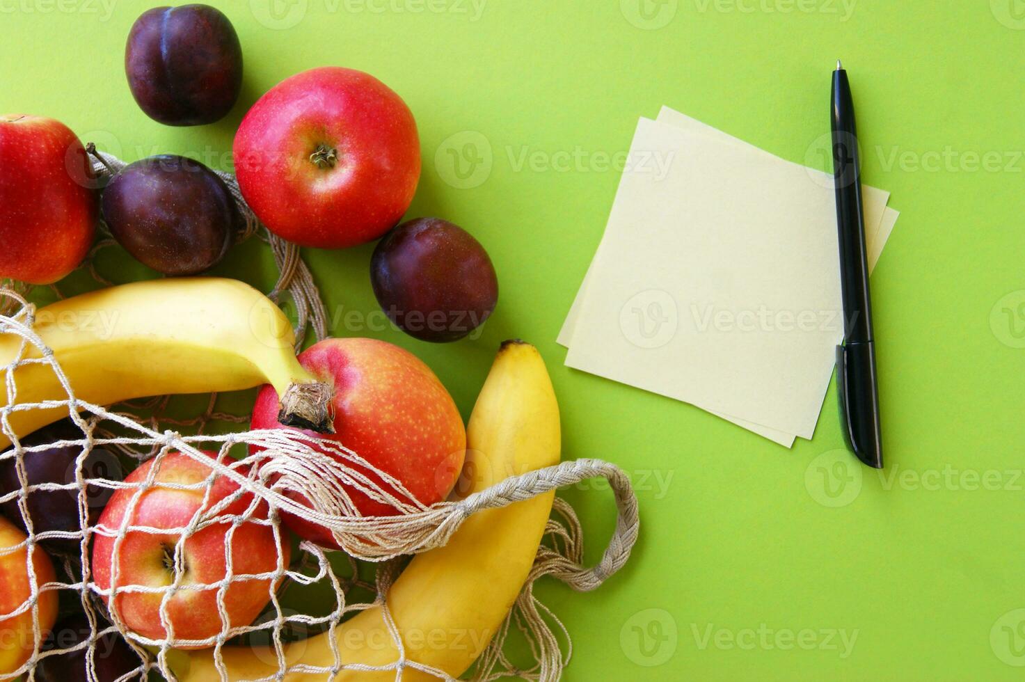 Red apples, bananas, plums, string bag and blank paper with black pen ...