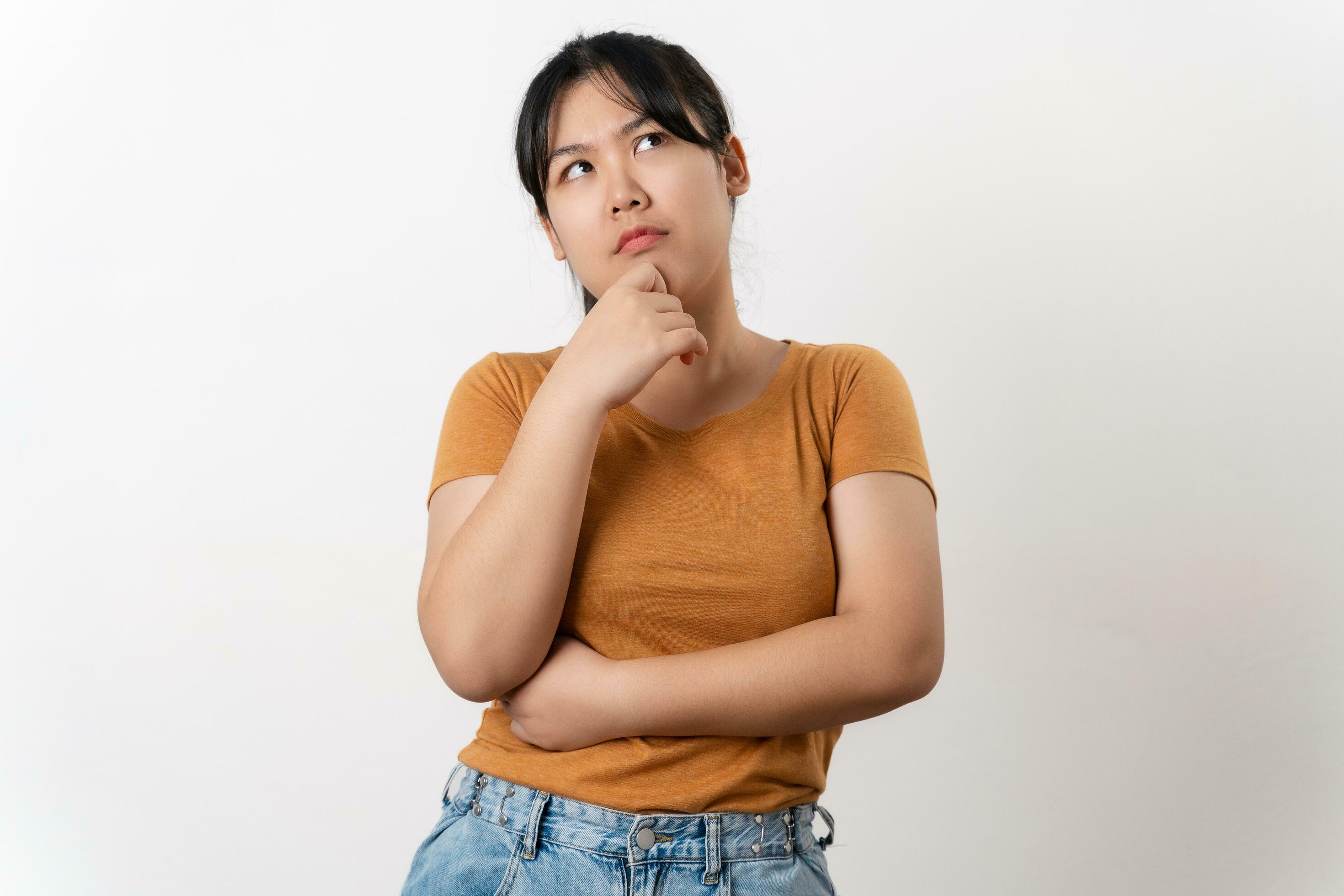 The curious thoughtful young Asian woman looks pensively standing on ...