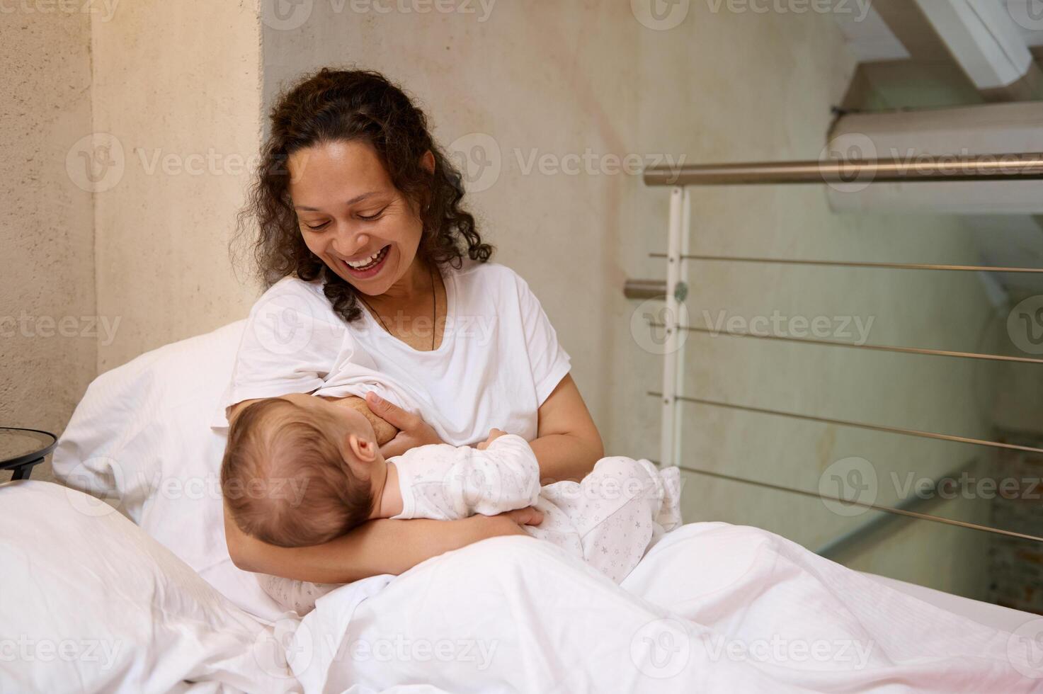 Happy mother smiles breastfeeding newborn baby, expresses positive emotions, feels emotional ...