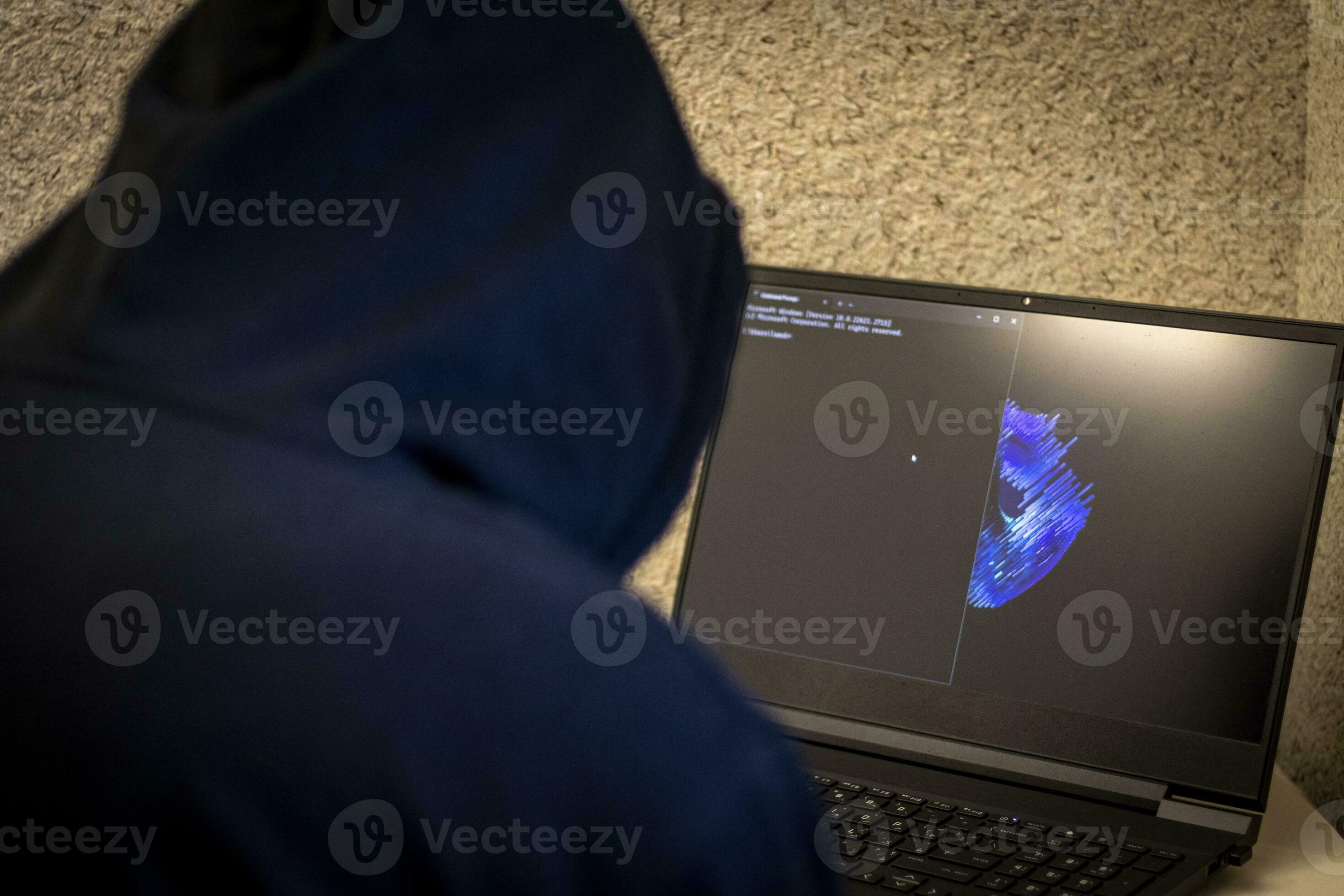 Man looked like hacker in a hood sitting in the front of laptop ...