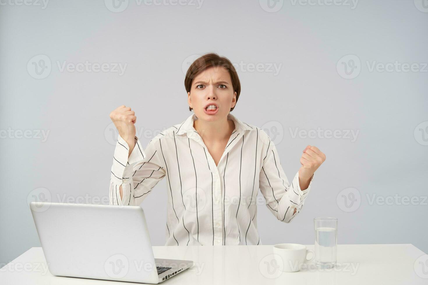 Angry Young Brown Eyed Short Haired Brunette Female With Casual Hairstyle Clenching Fists And