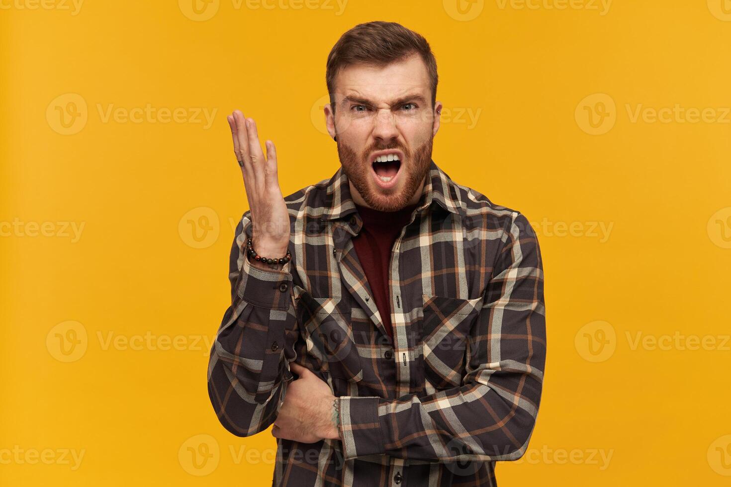 Furious angry young man in plaid shirt with beard and raised hand looks ...