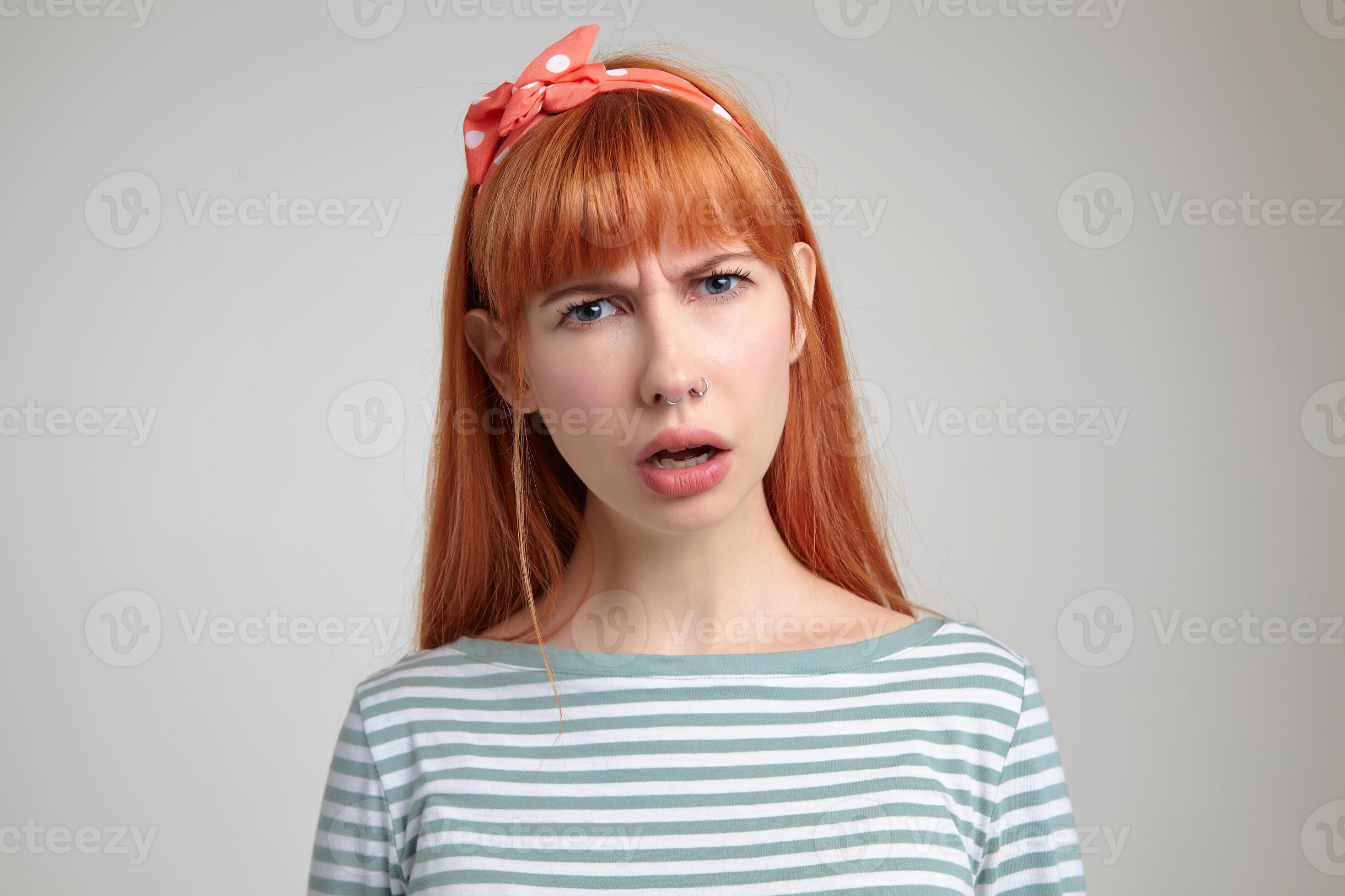 Indoor portrait of young ginger female posing over white wall looking ...