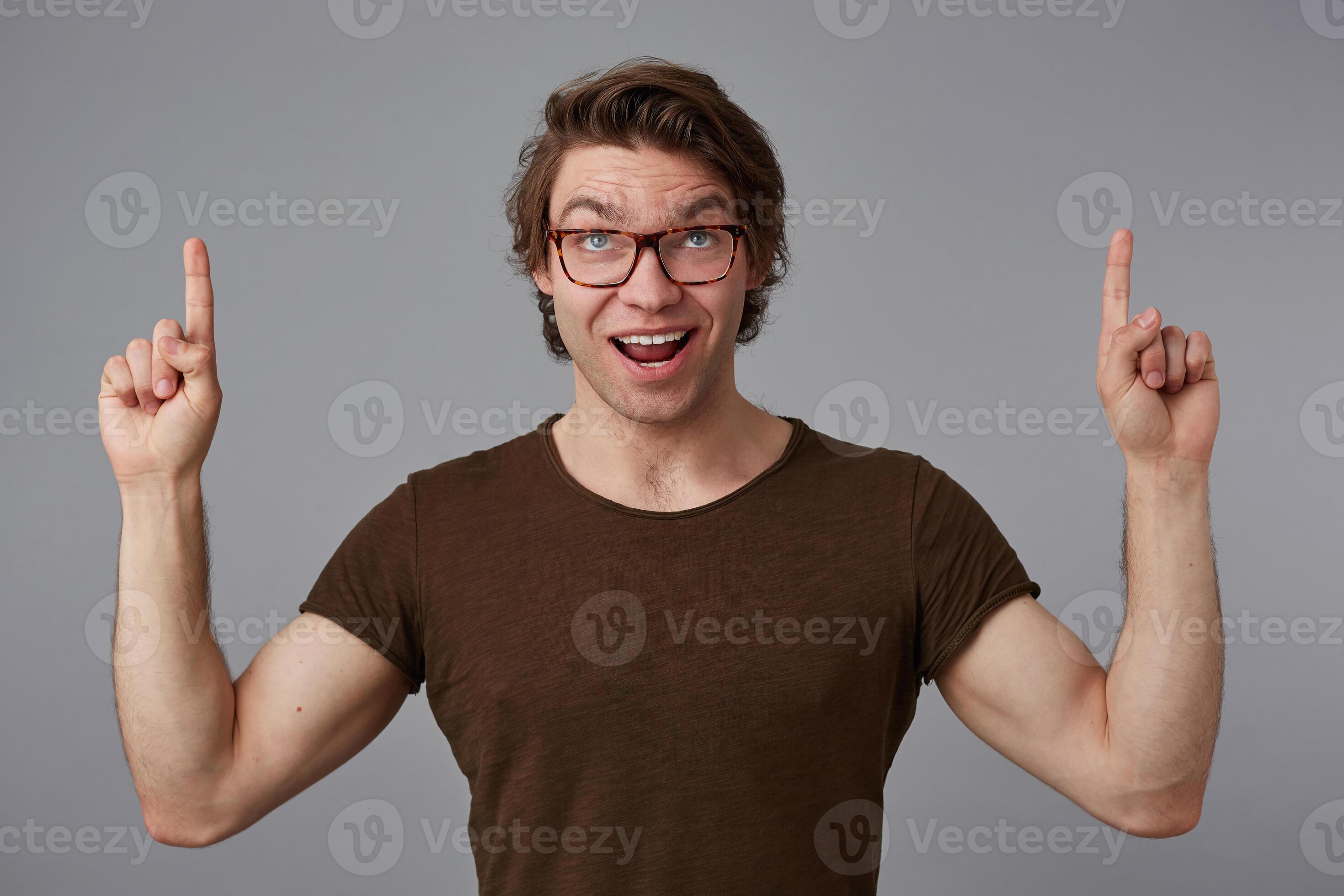 Portrait of young happy amazed guy with glasses, stands over gray background with surprised ...