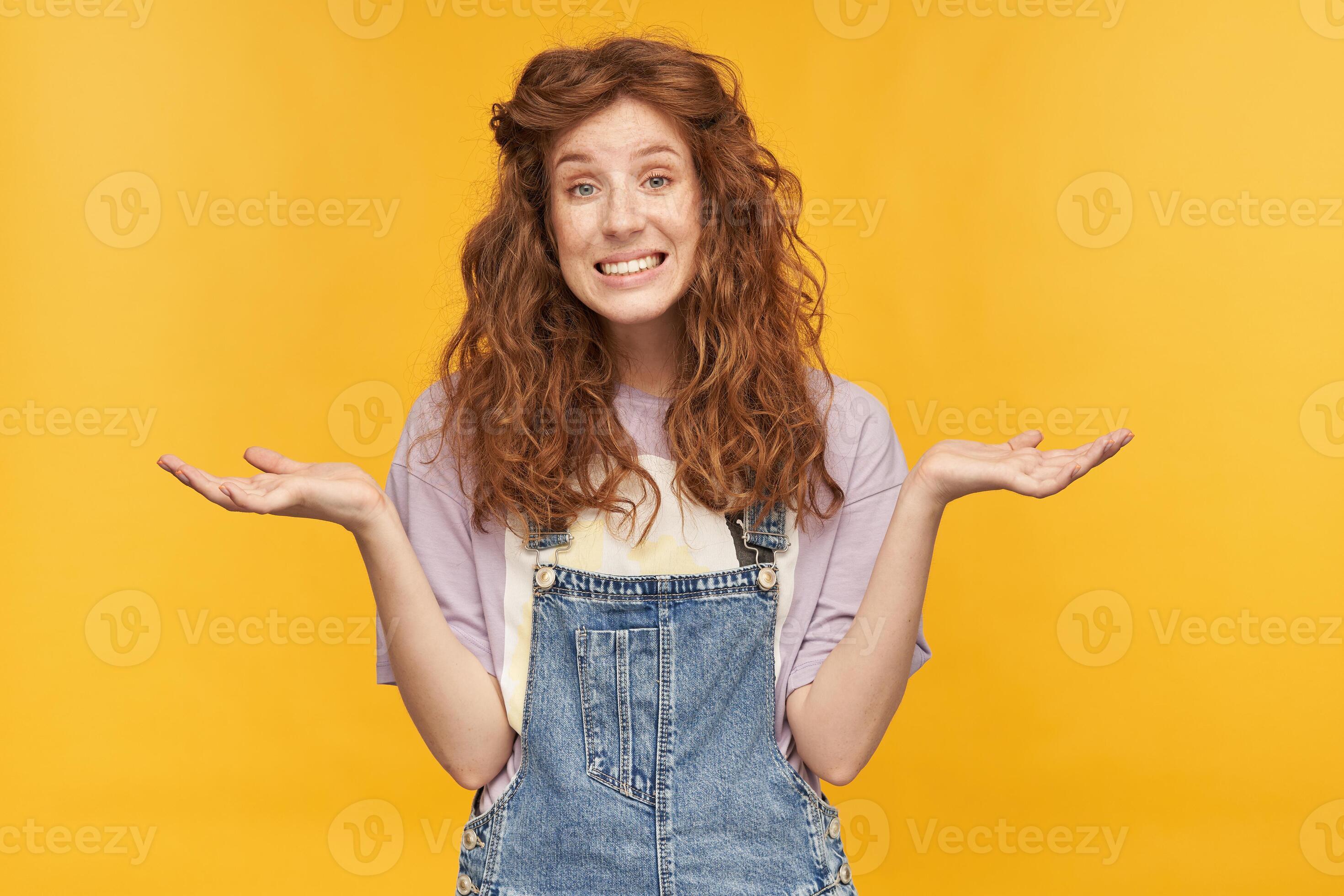 Unsure, uncertain young ginger female, with a wavy long hair, smiles ...