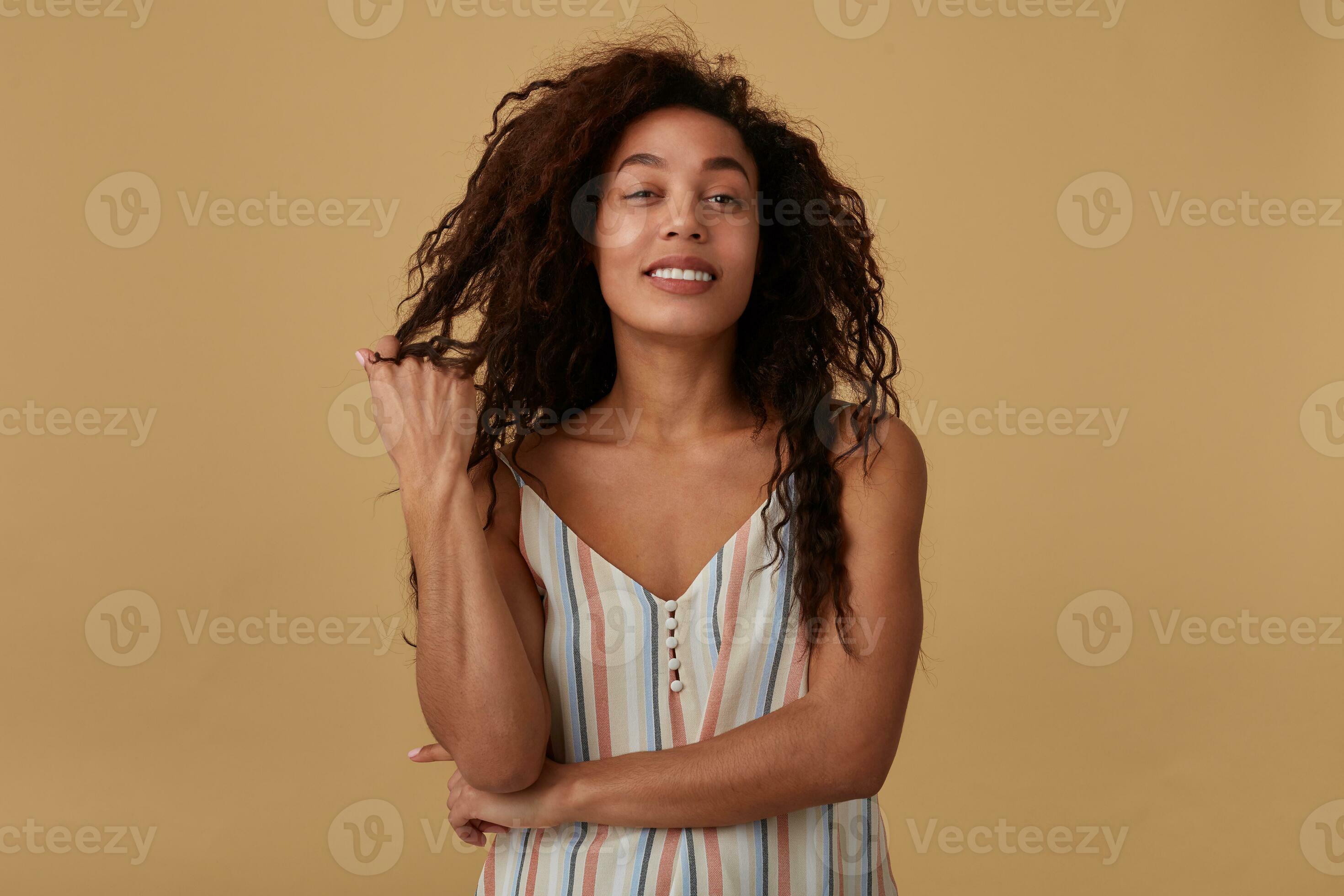 Glad Young Attractive Long Haired Curly Dark Skinned Woman Twisting Her