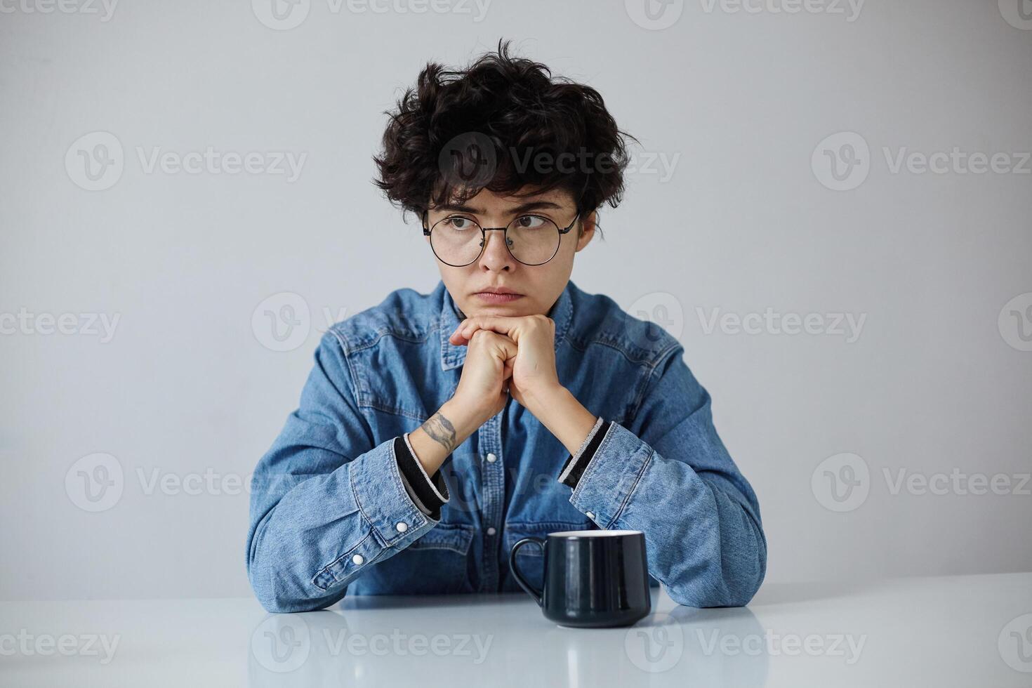 Pensive young brown-eyed short haired curly brunette woman in eyeglasses holding her head on ...